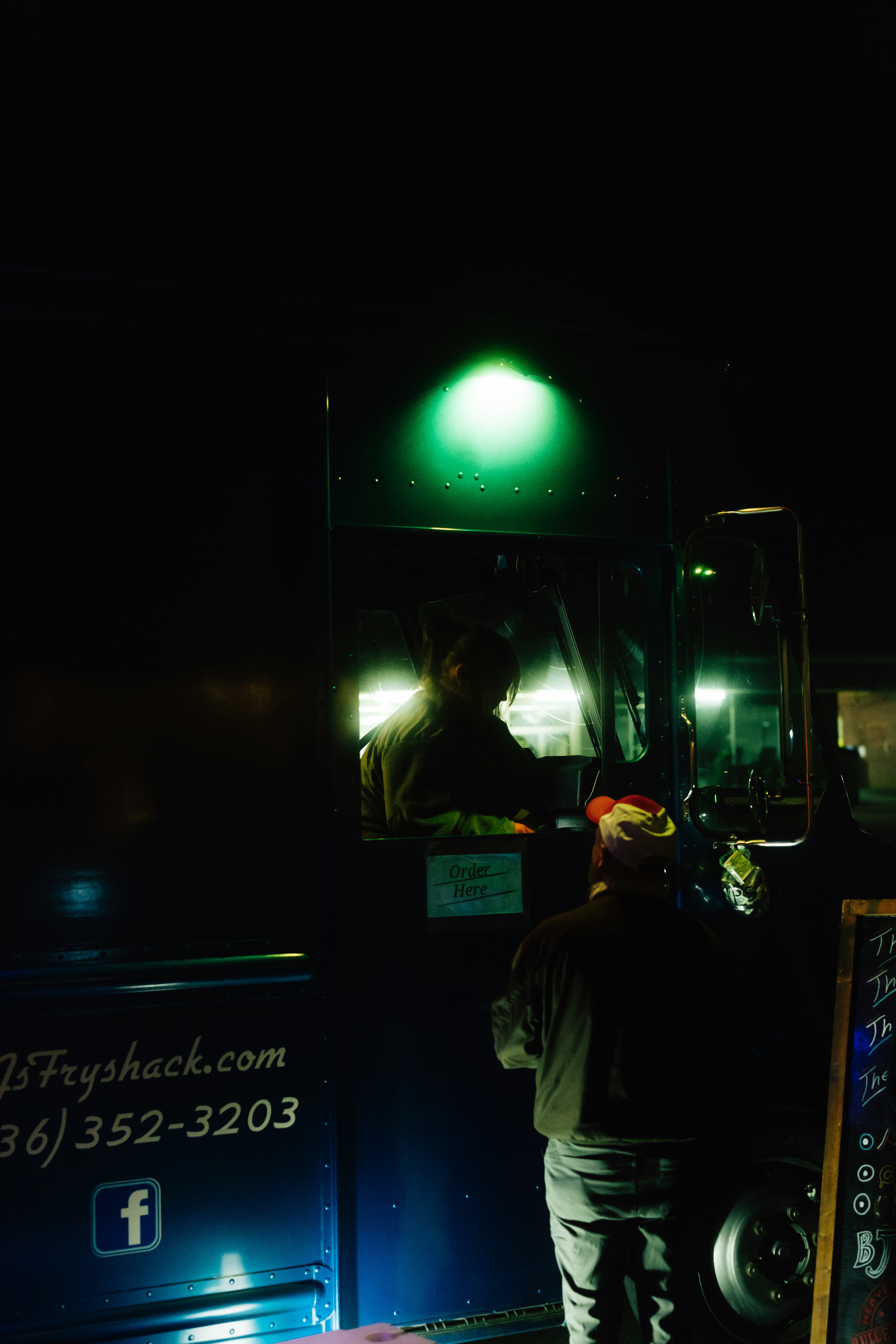 People ordering food from a dark food truck at night.
