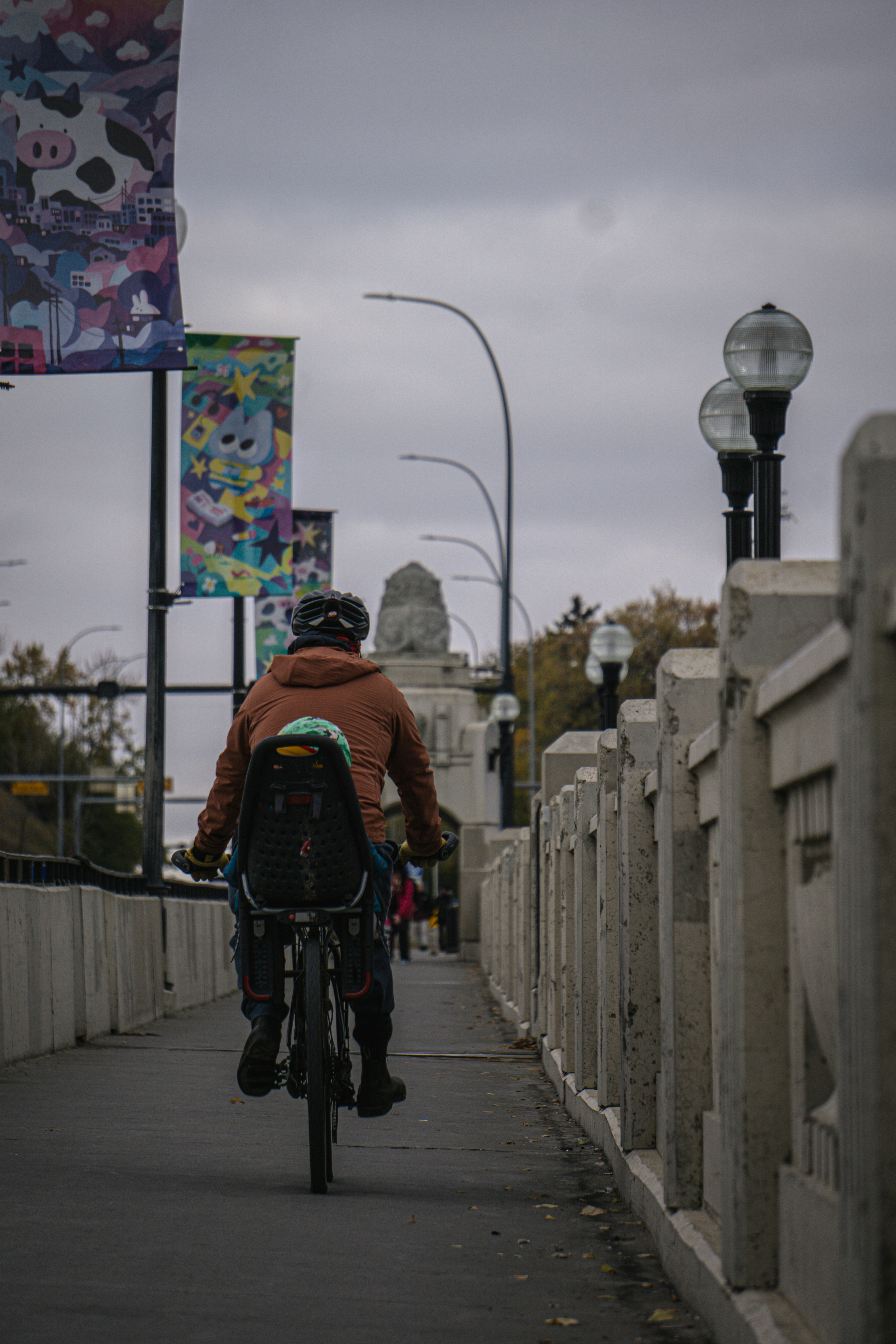 Person rides bicycle with child on bridge.