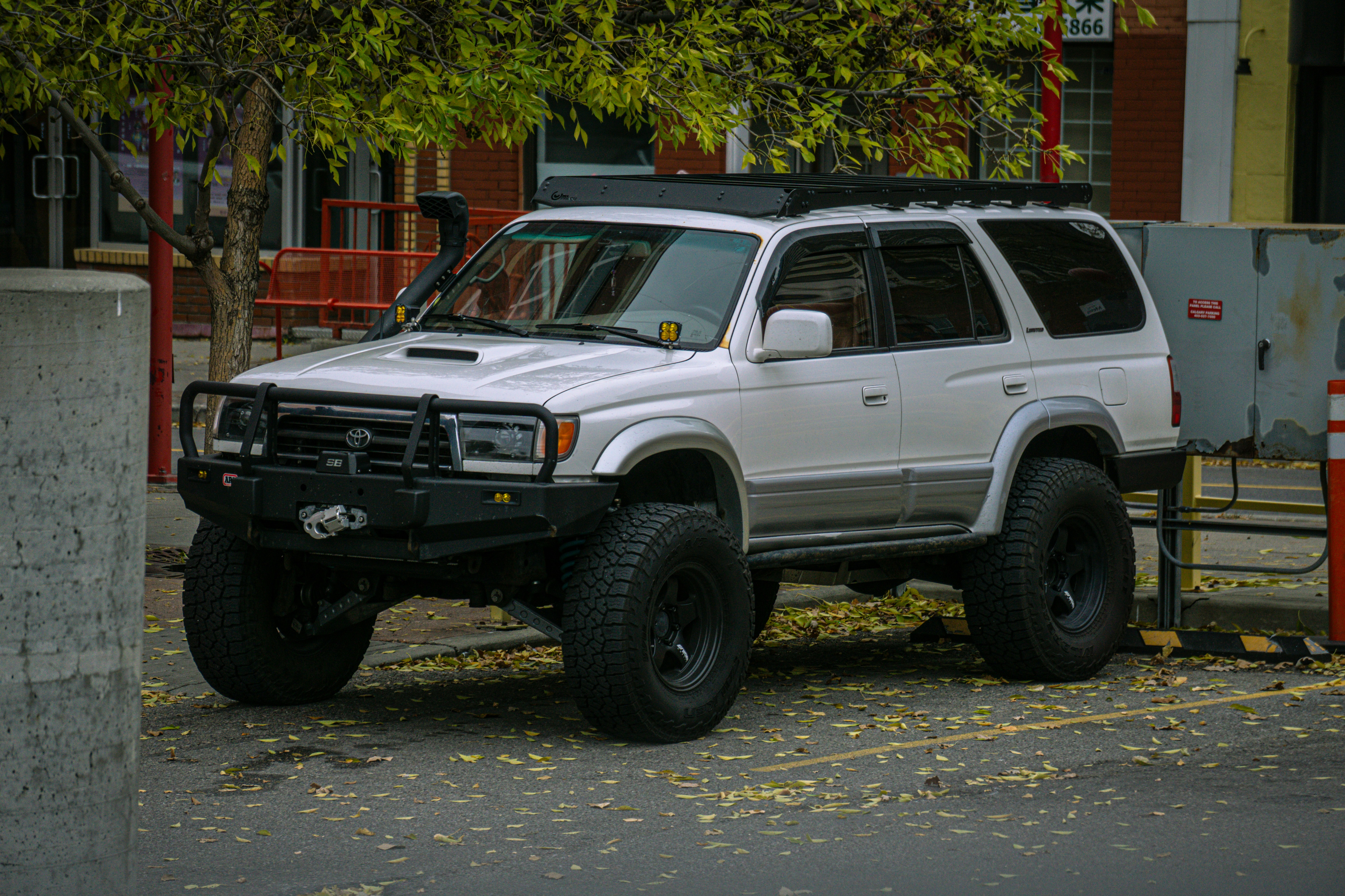 Modified SUV parked on a city street, showcasing off-road capabilities with oversized tires and a robust front bumper.