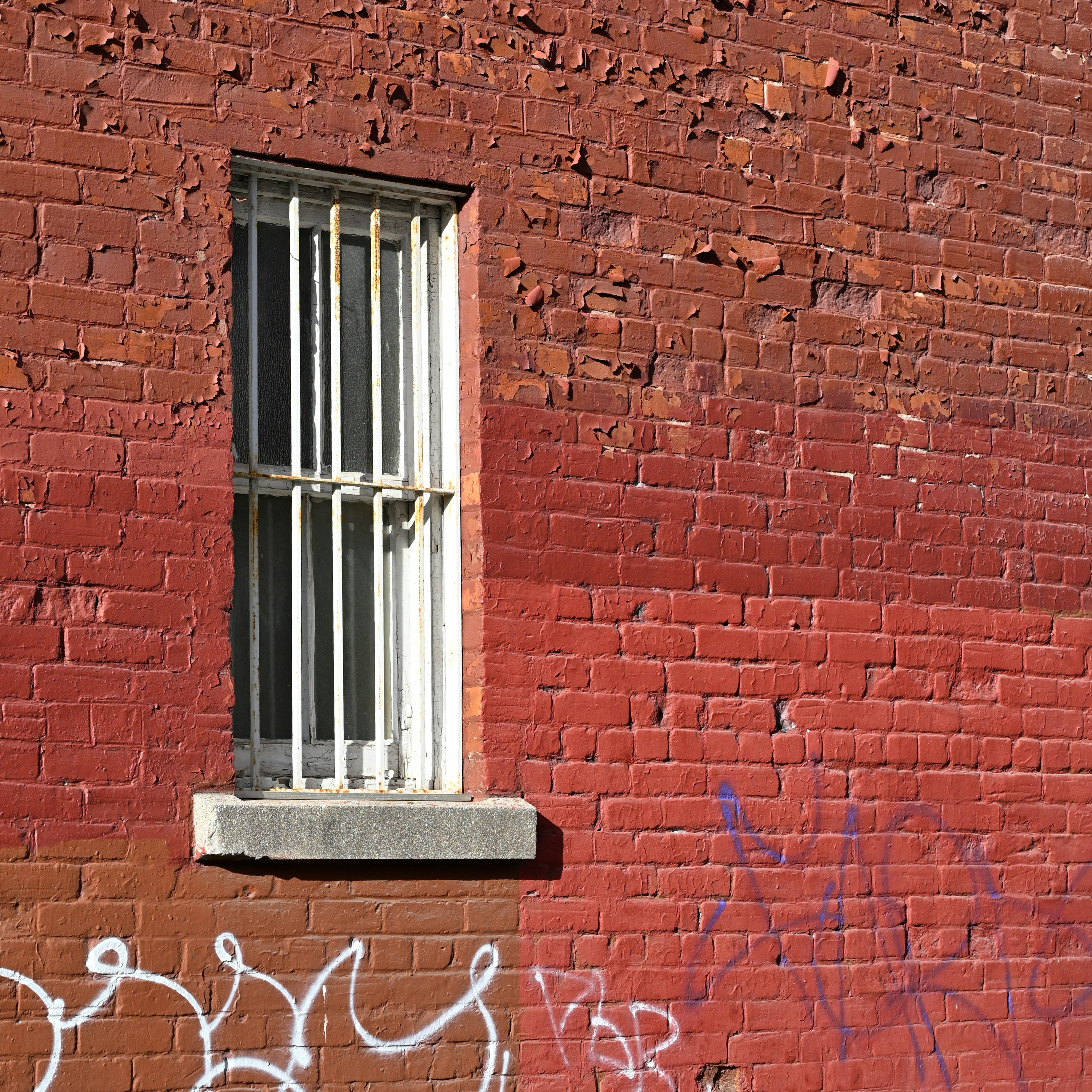 Red brick wall with a barred window and graffiti.