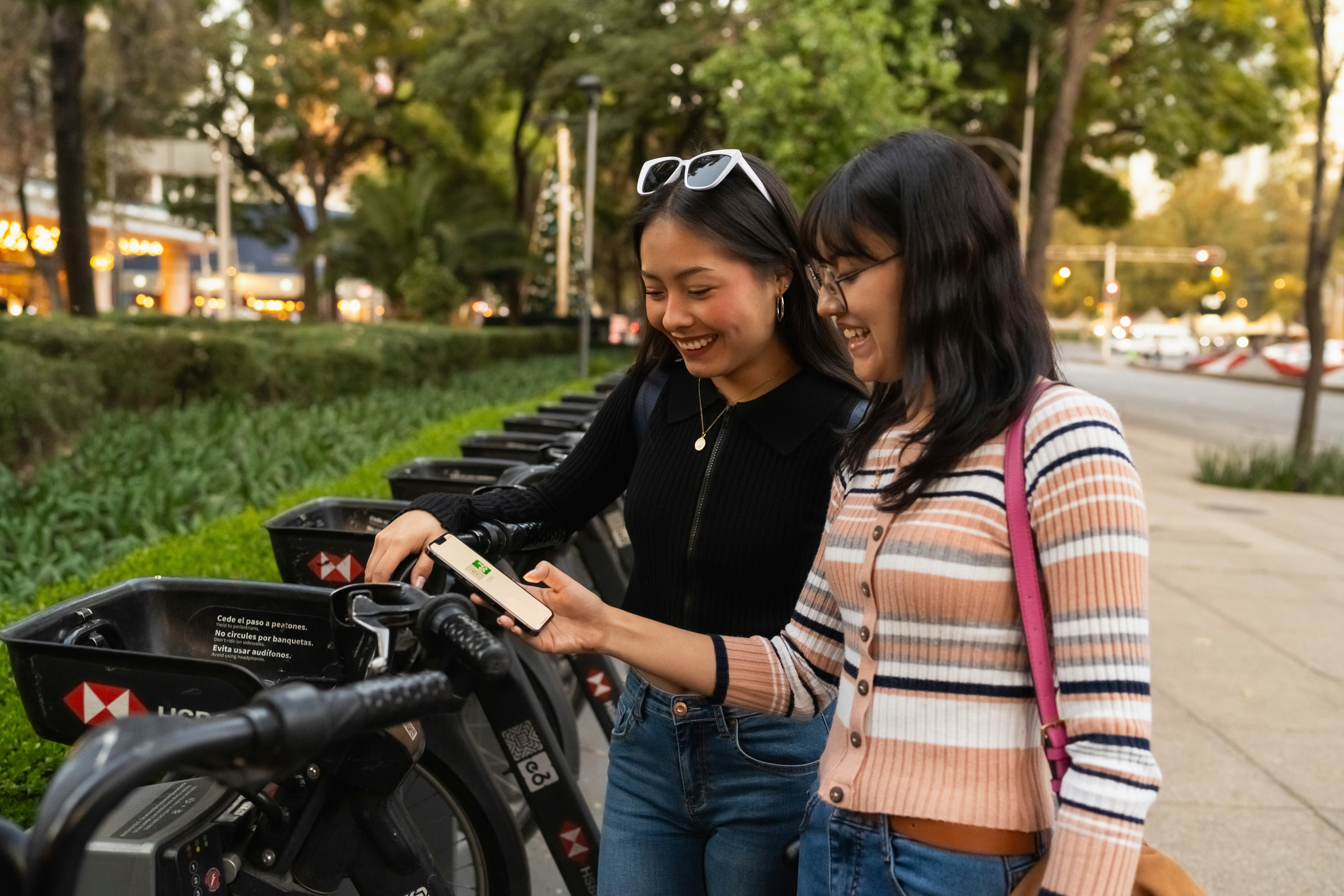 Two women looking at phone near bike share station