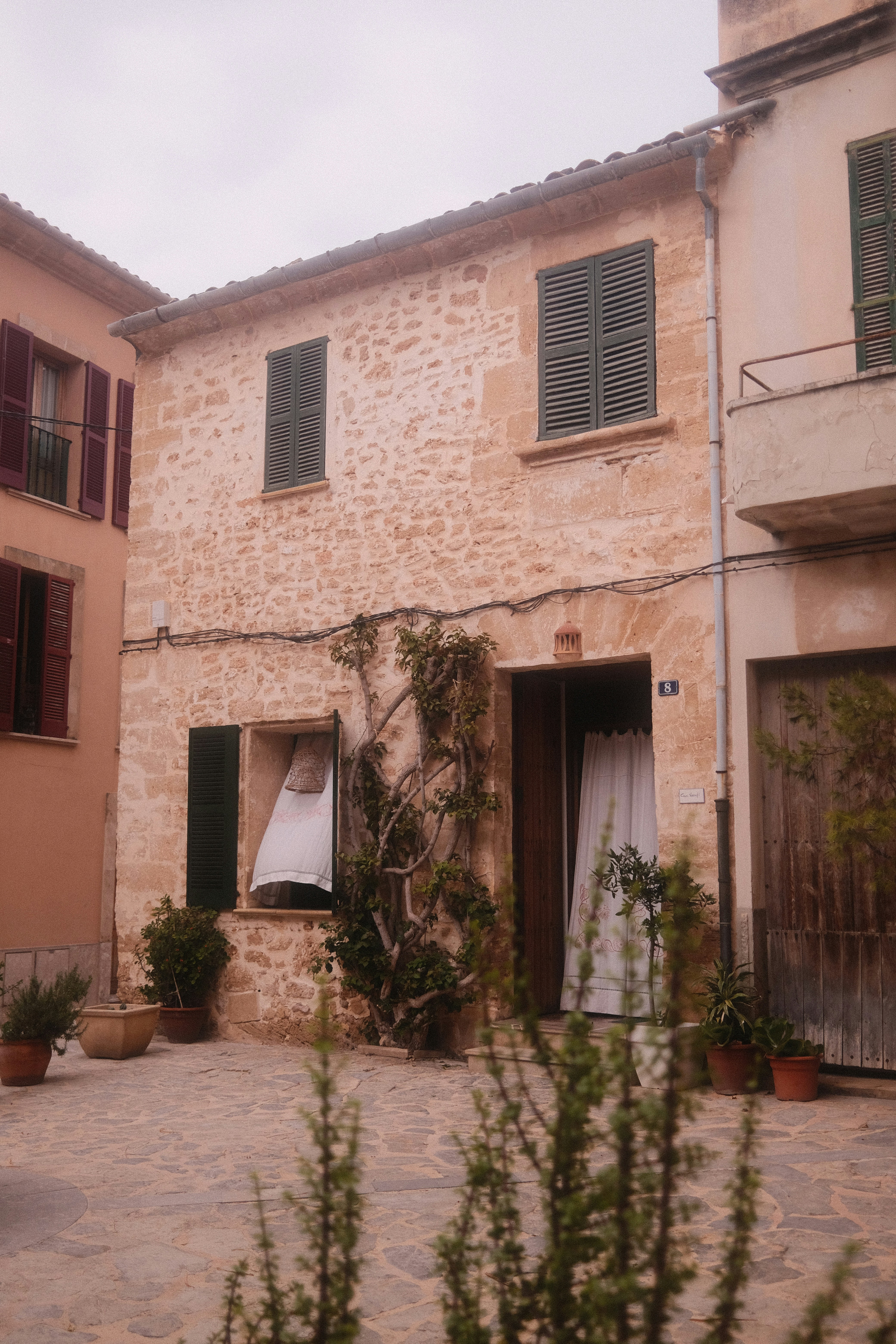 Stone building with green shutters and potted plants.