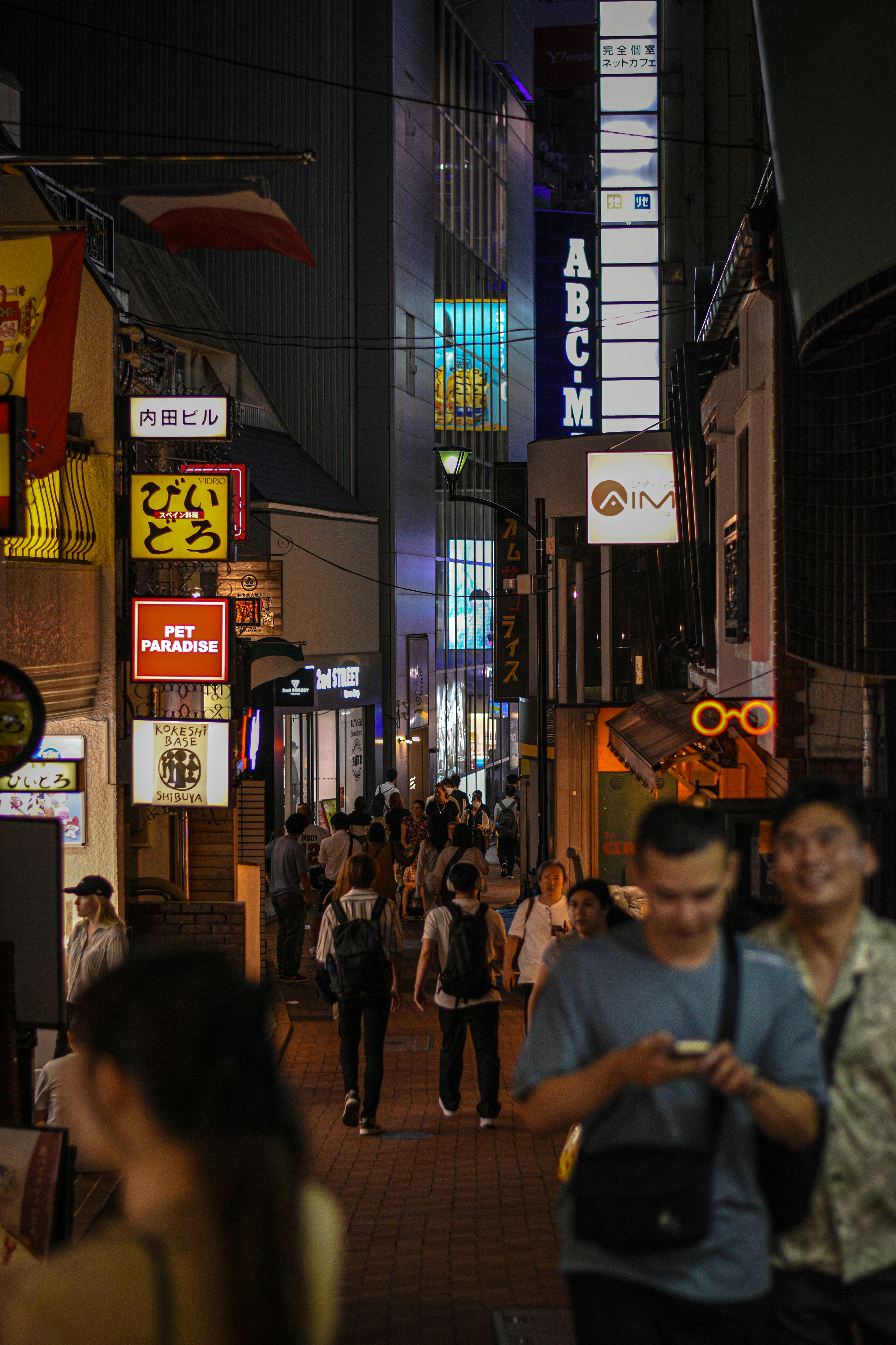 Bustling street filled with people and vibrant shop signs in a lively urban setting at night.