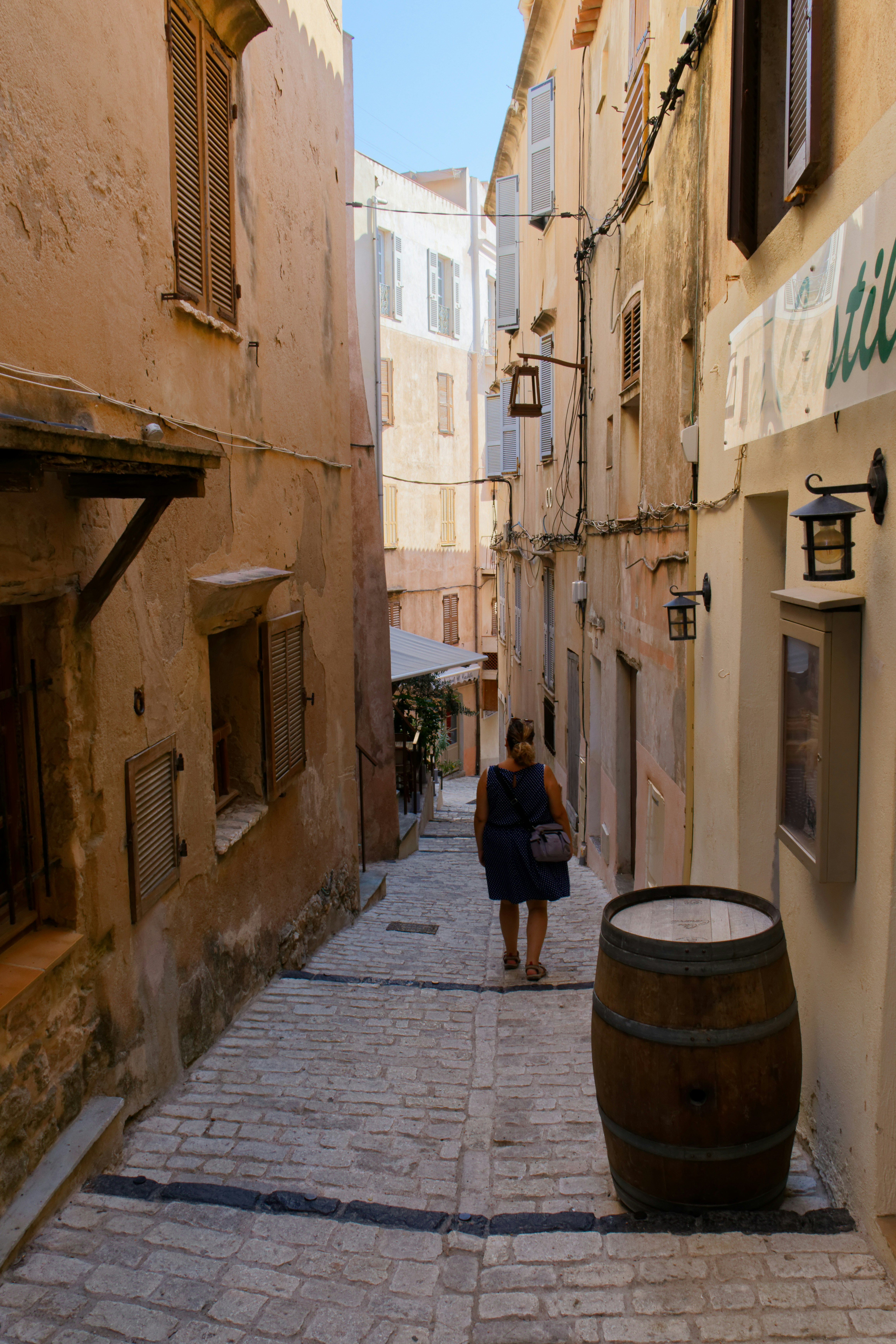 A woman walks down a narrow cobblestone street.