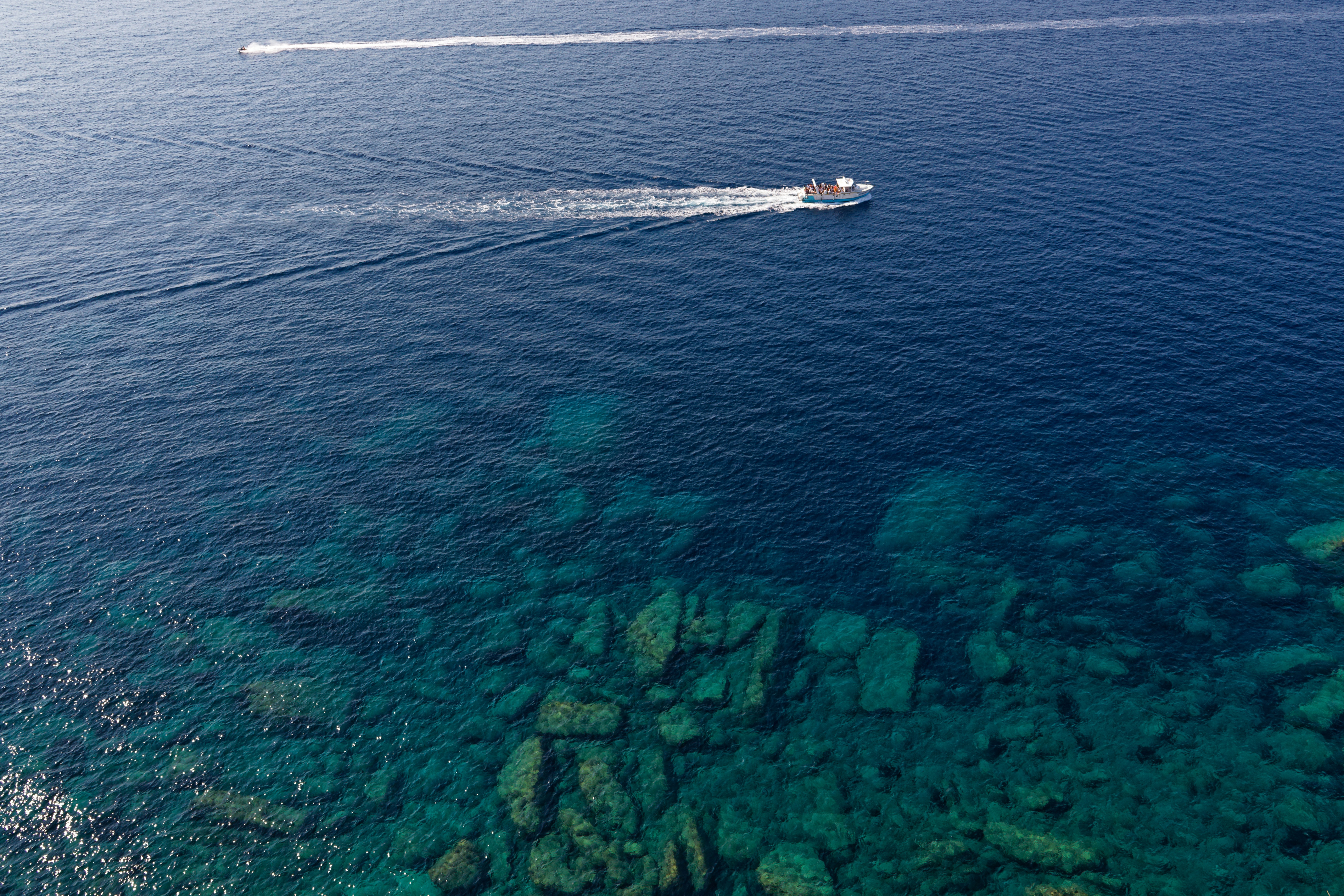 Two boats sail across the clear blue ocean water.