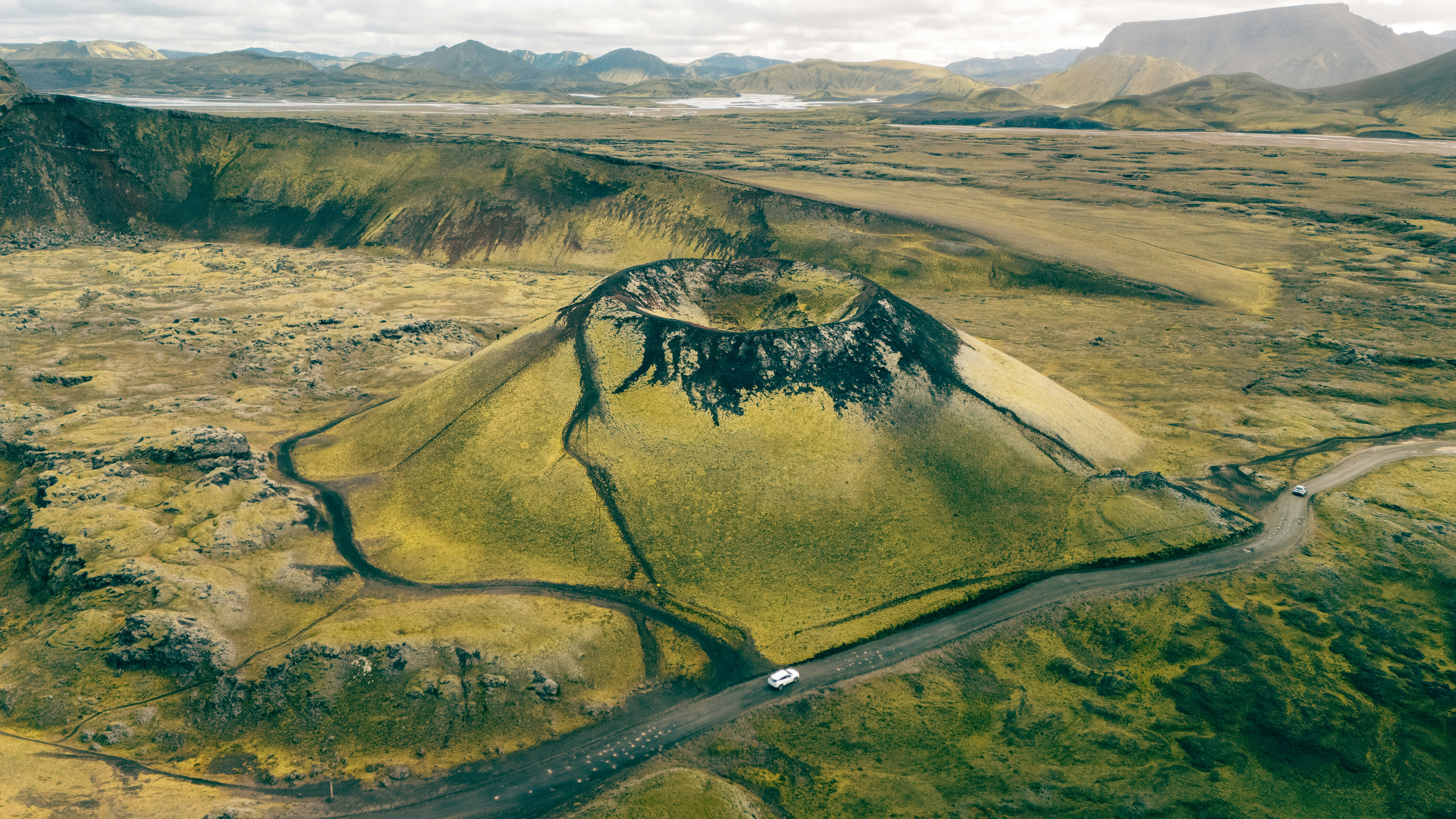 Aerial view of a vibrant green volcanic crater surrounded by rugged terrain, showcasing the unique geological features of the landscape.
