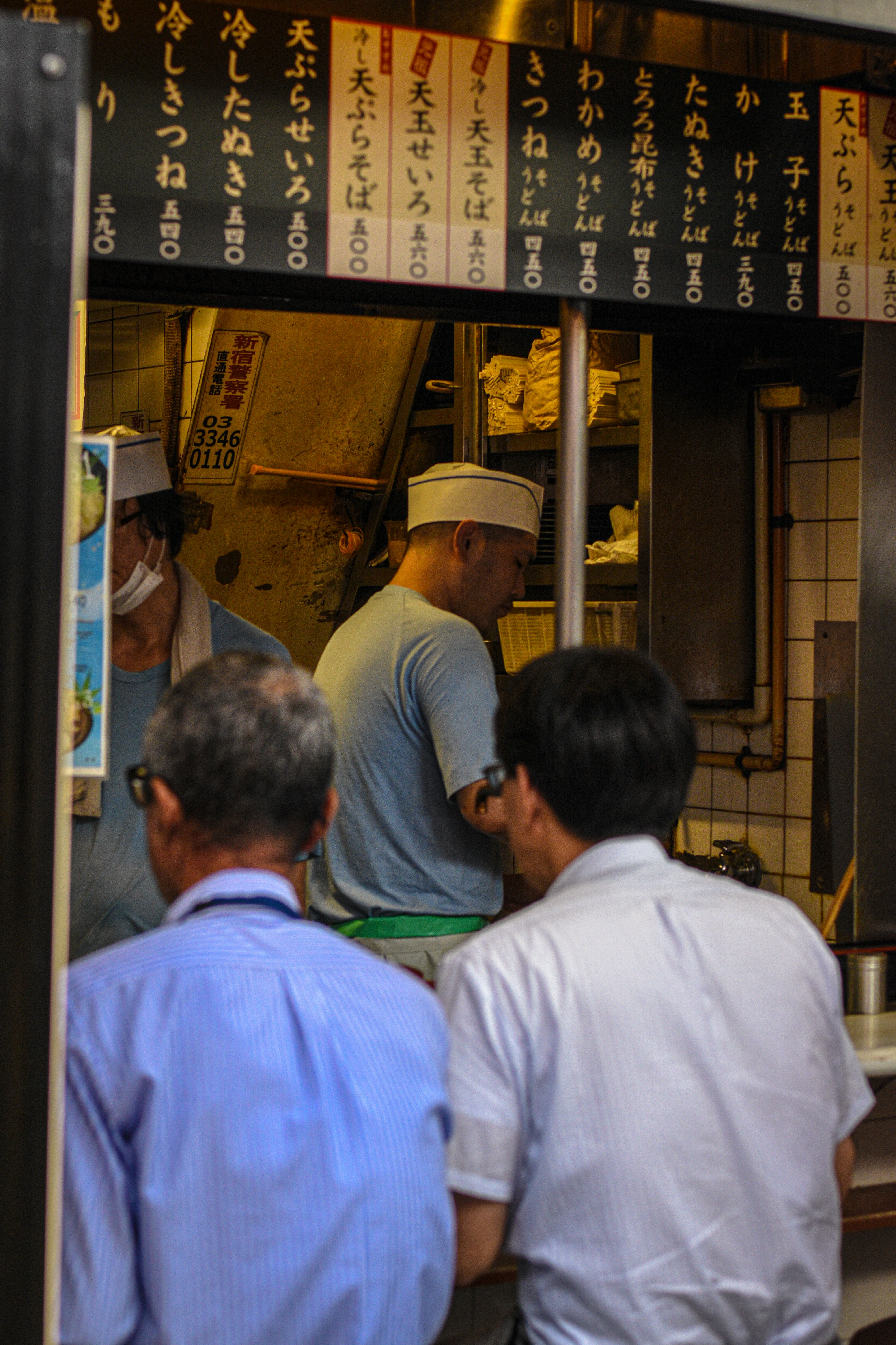 Chefs prepare food behind a counter with japanese menu.
