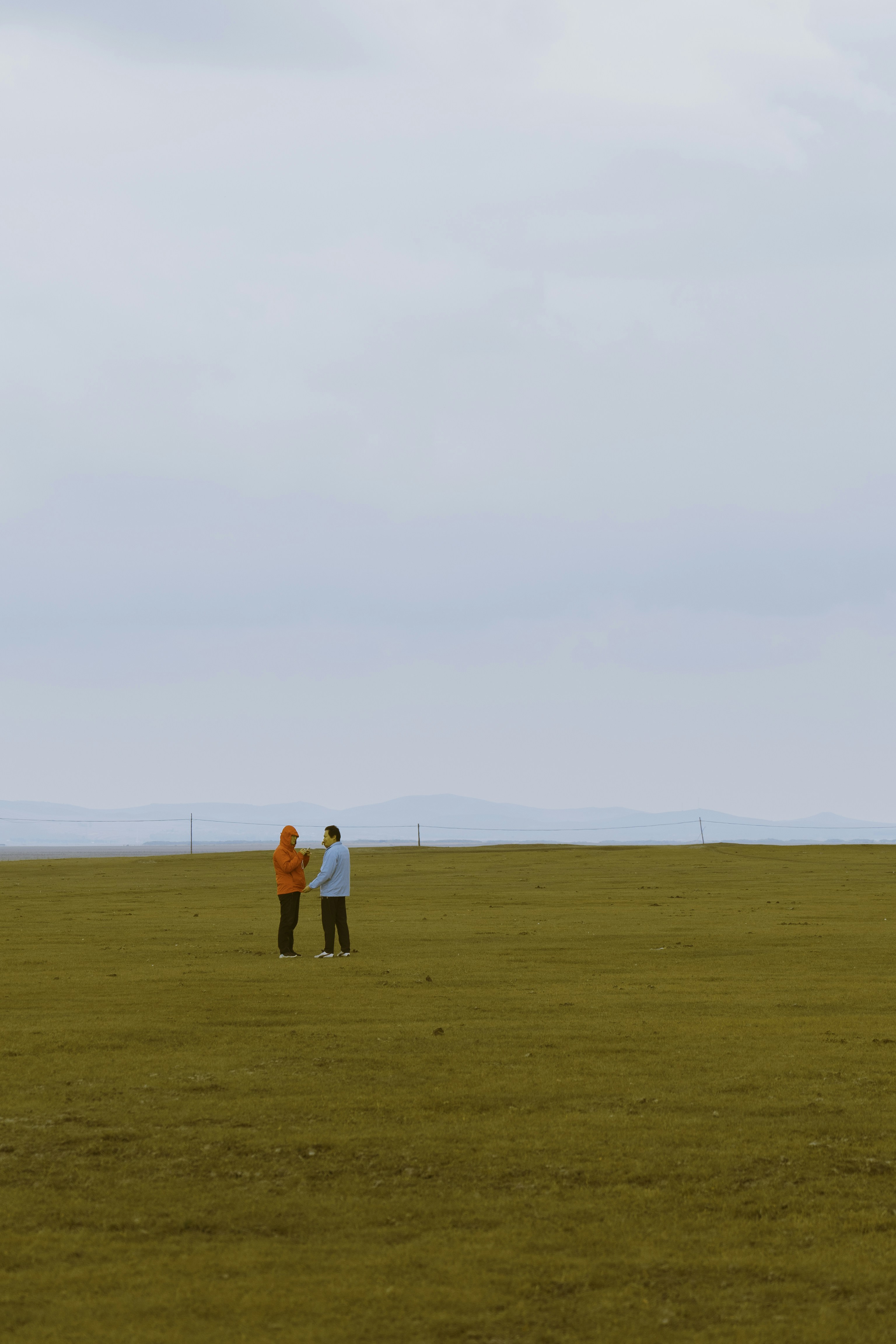 Two people standing in a vast grassy field.