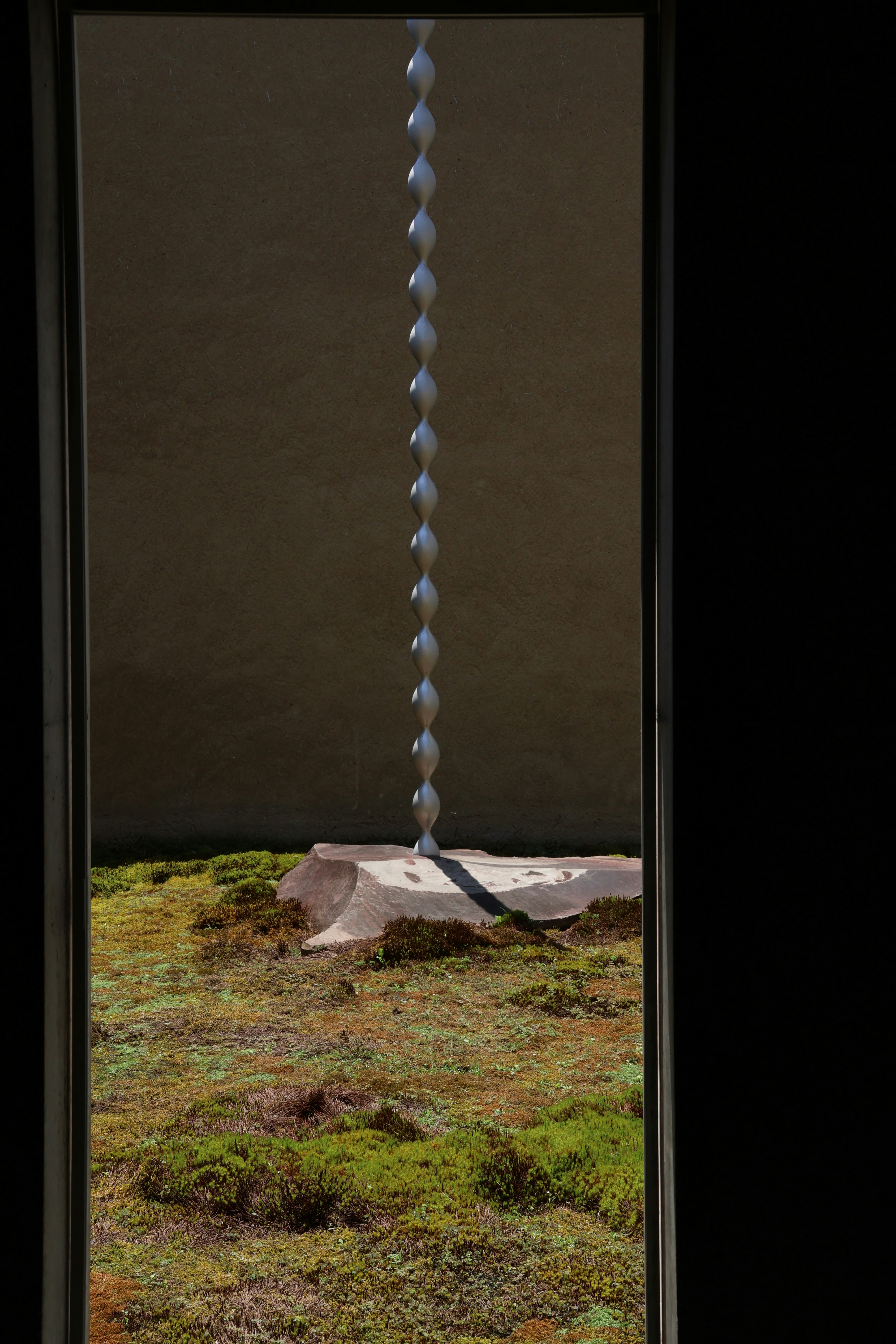 An art installation drilling towards the ground | A decorative metal chain hanging over mossy mossy ground.
