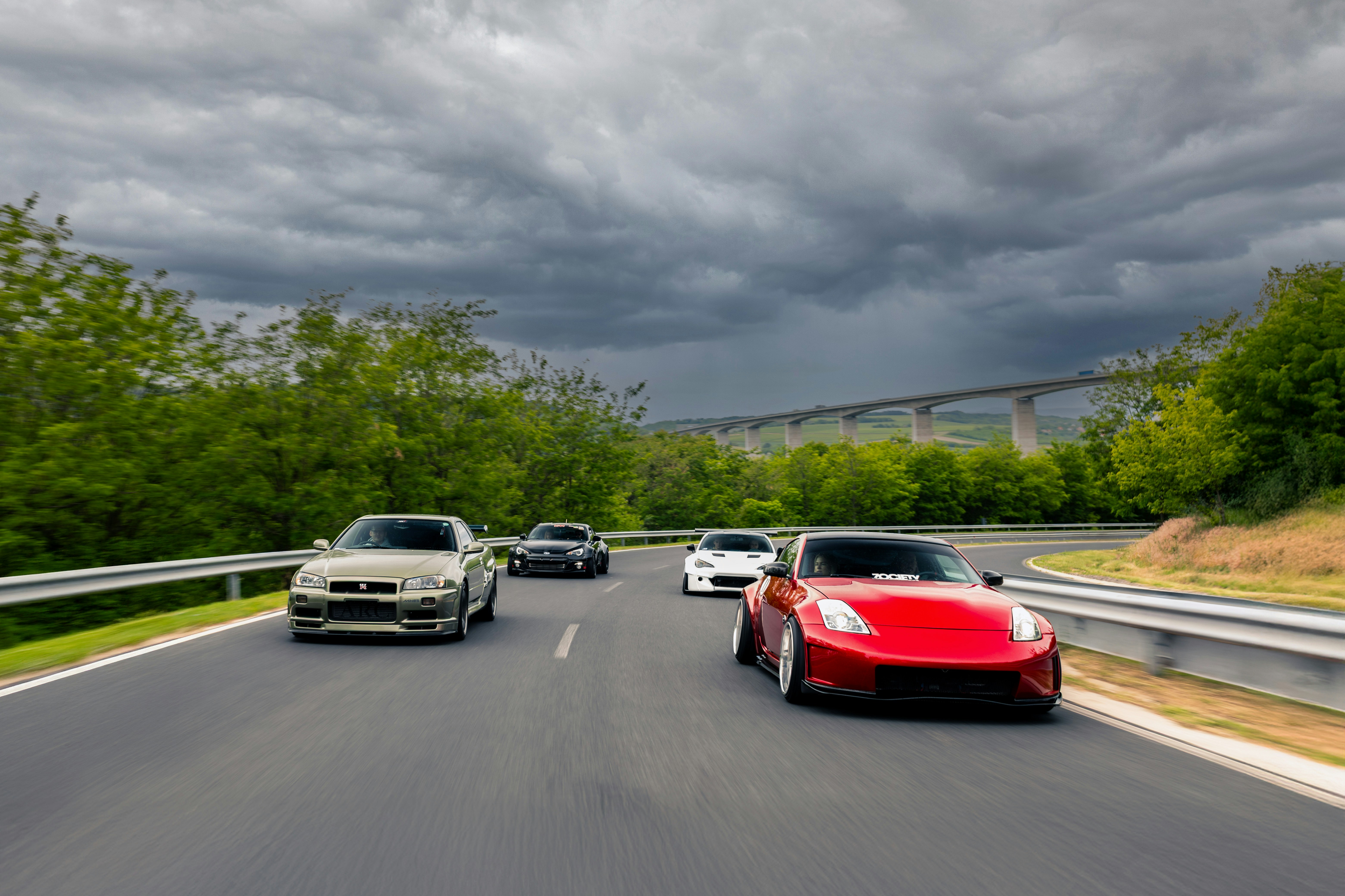 Several cars driving on a winding road under stormy skies