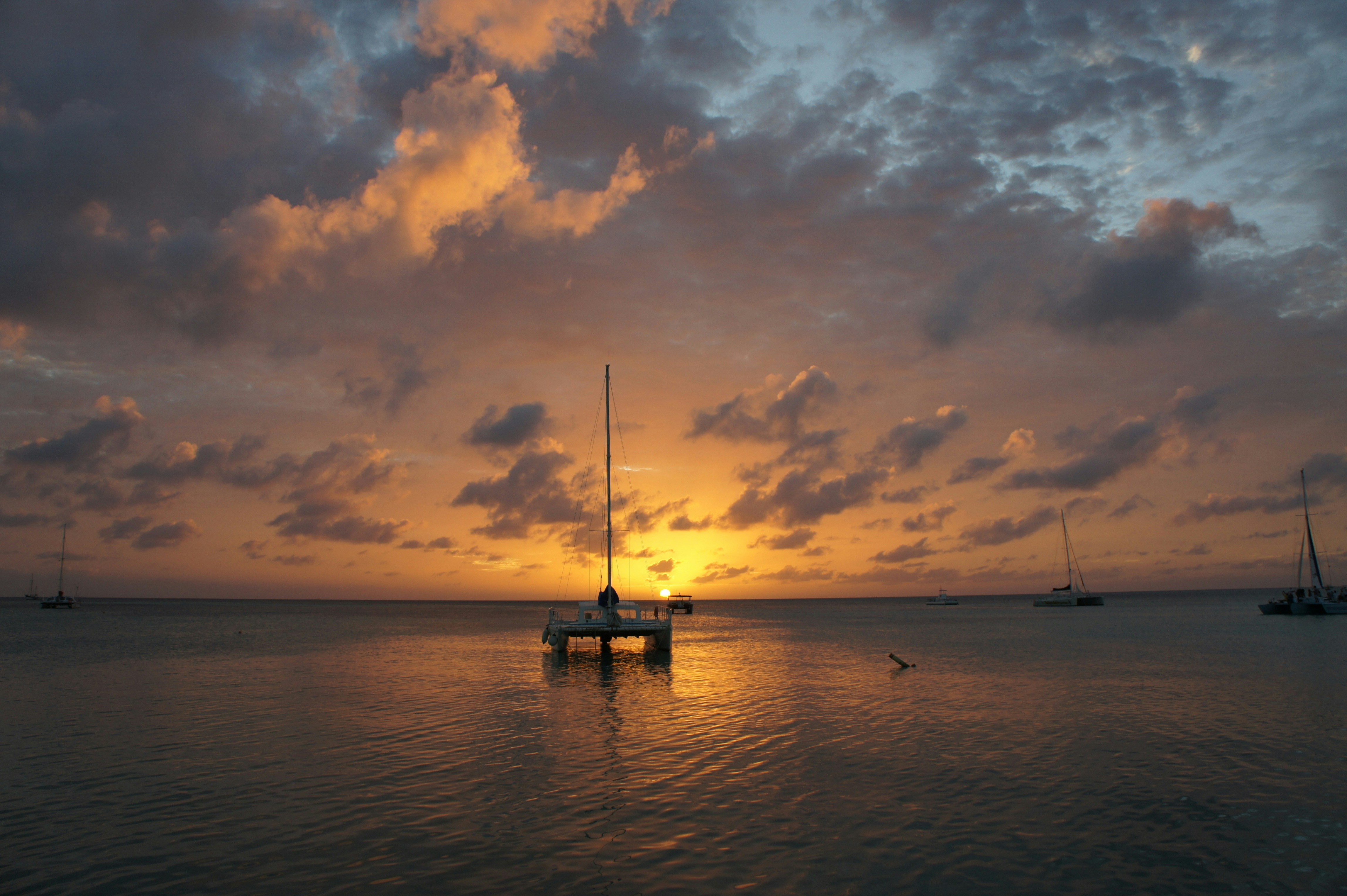Sailboats on the ocean at sunset with dramatic clouds.