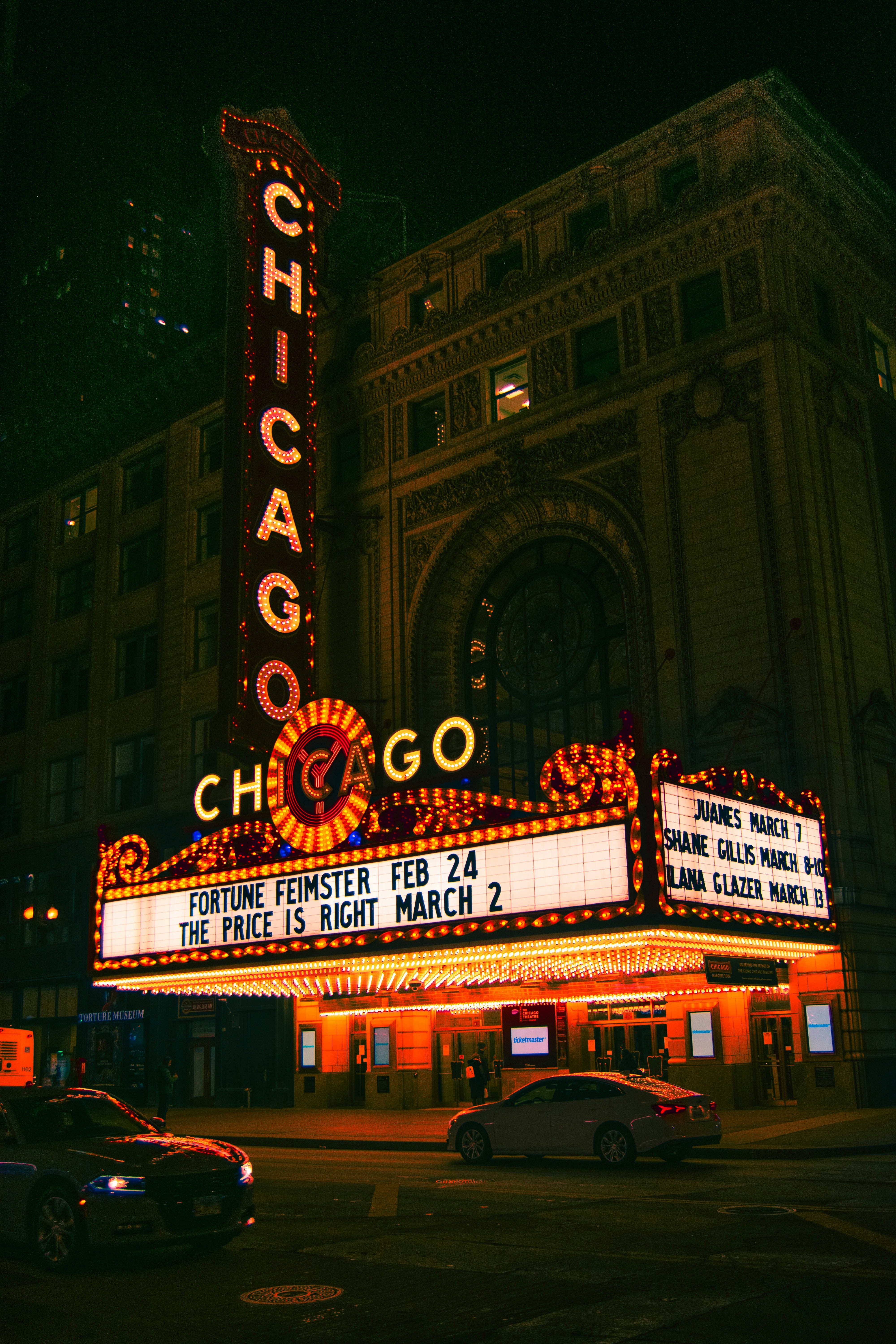 The chicago theatre illuminated at night with cars passing.