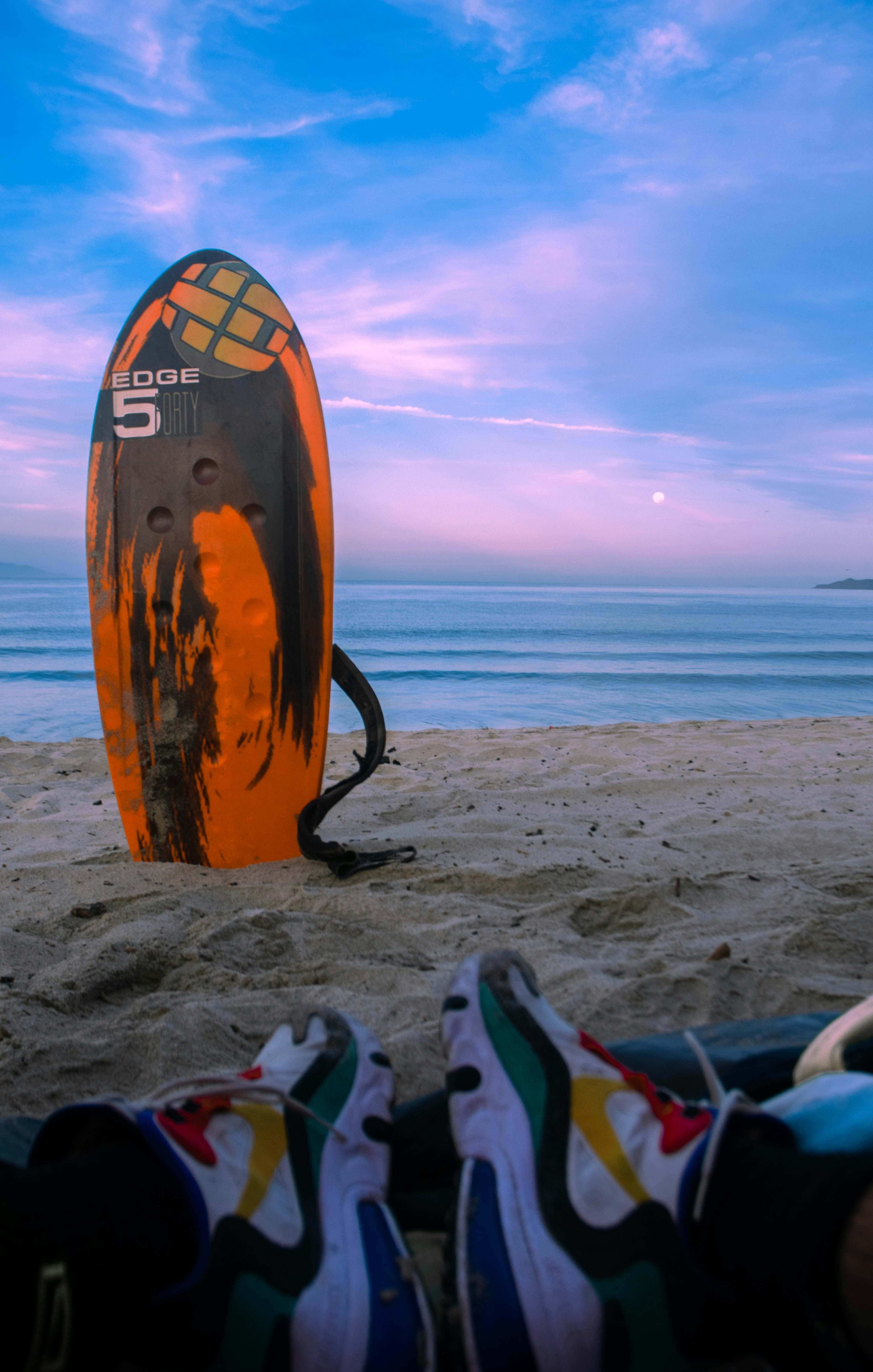 Orange boogie board on a sandy beach at sunset.