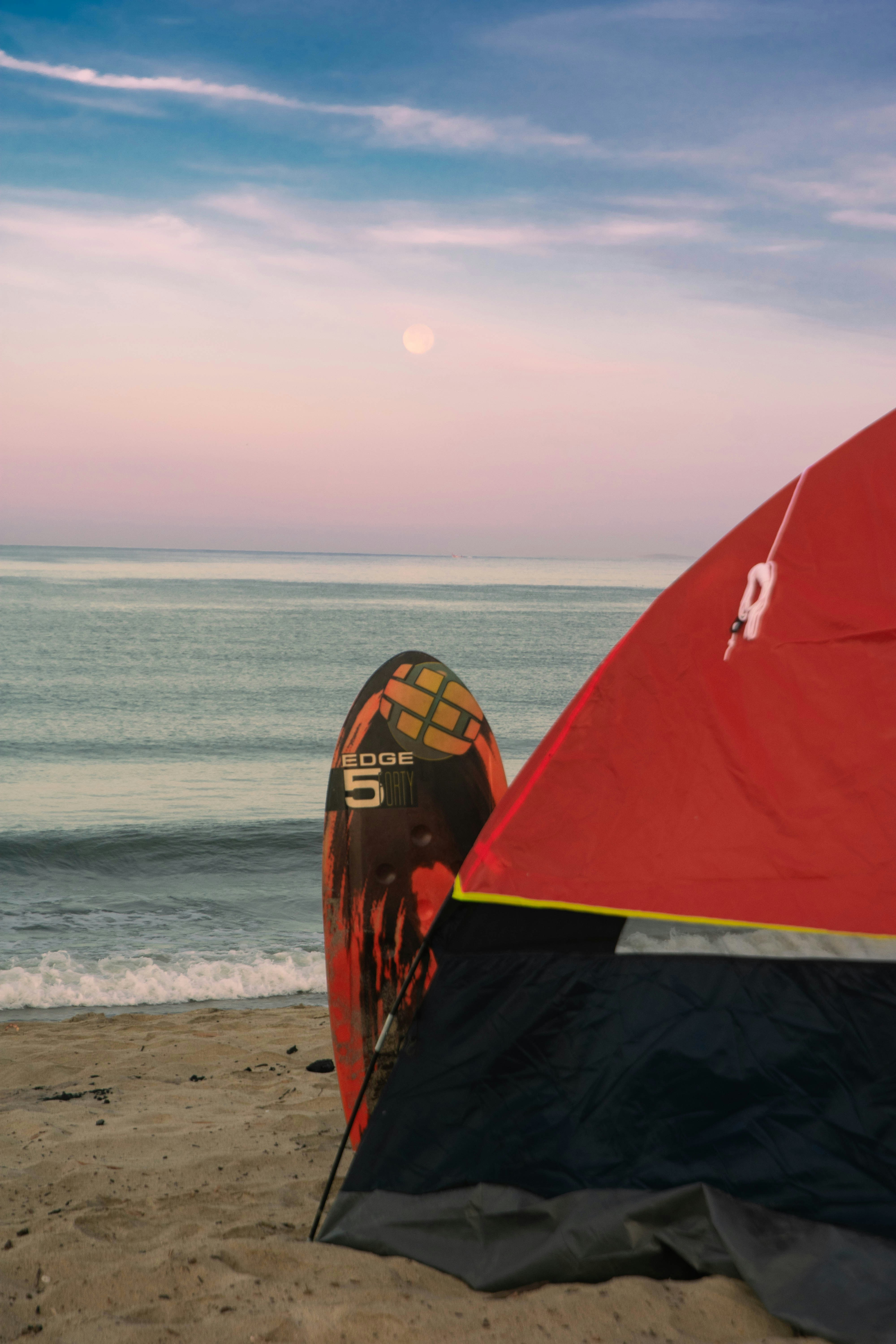 Tent and surfboard on beach with moonlit sky