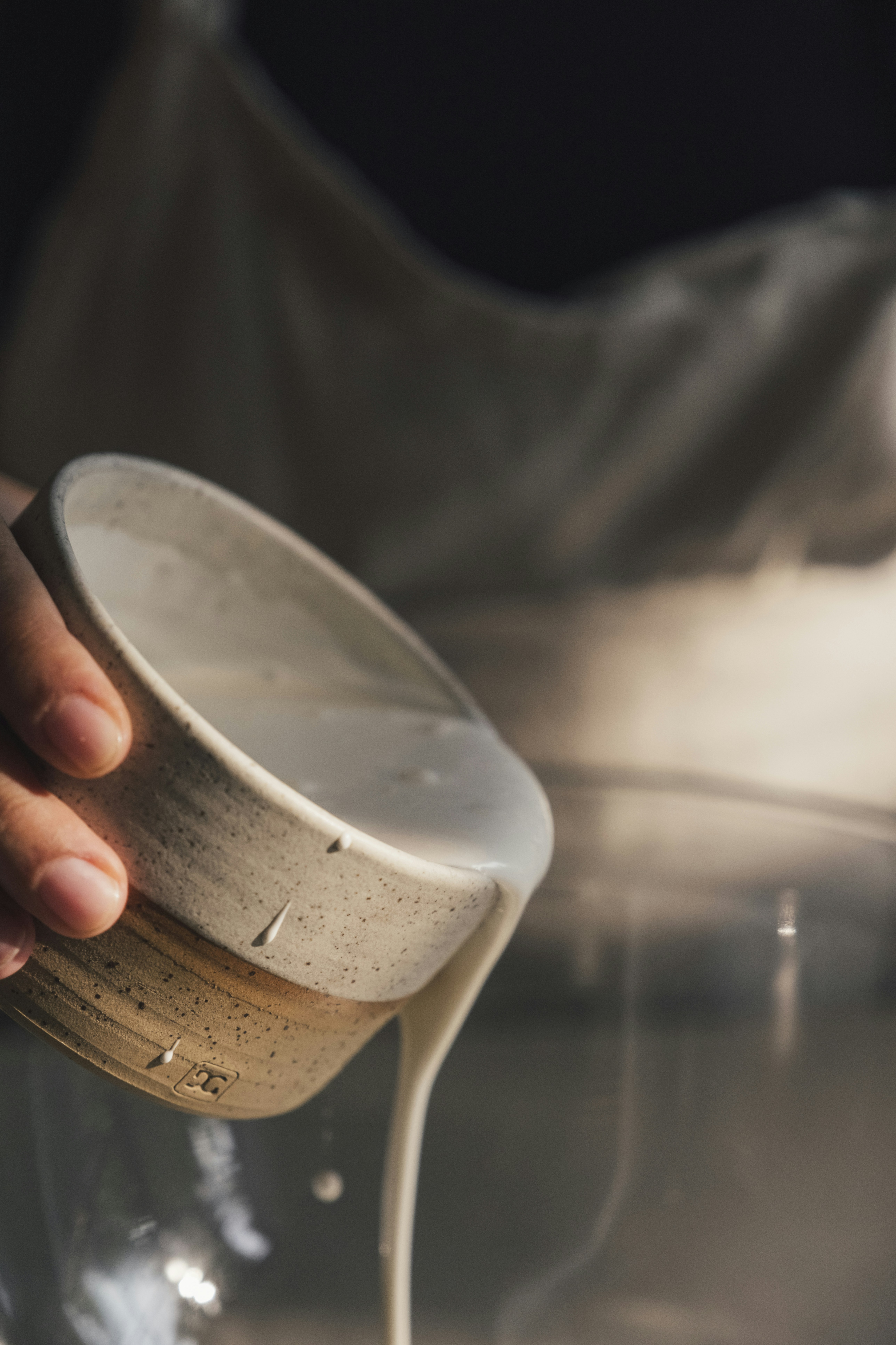 Hand pouring milk from a ceramic pitcher into a bowl.