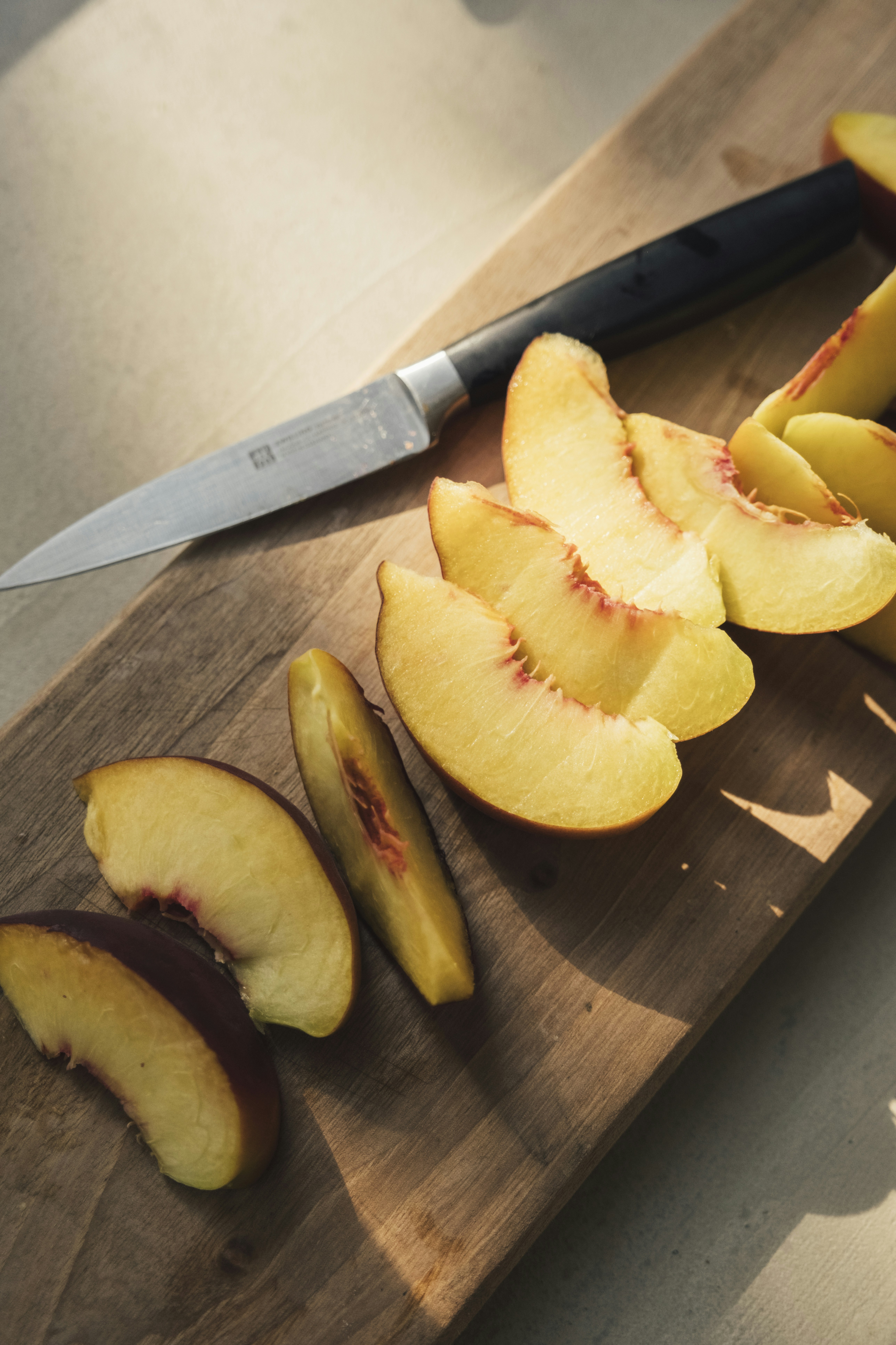 Sliced peaches and a knife on a wooden board.