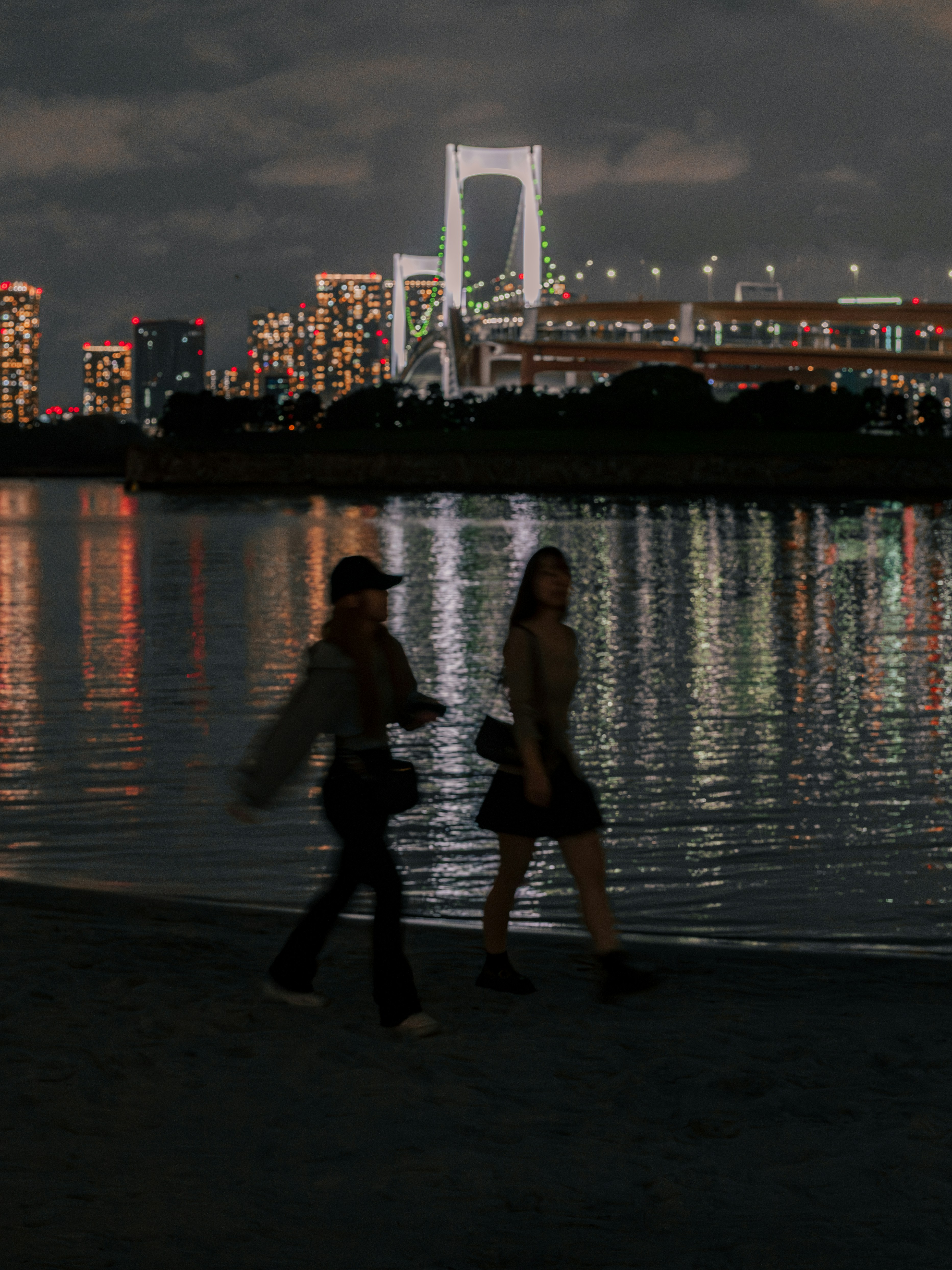 Two women walk along a waterfront at dusk.