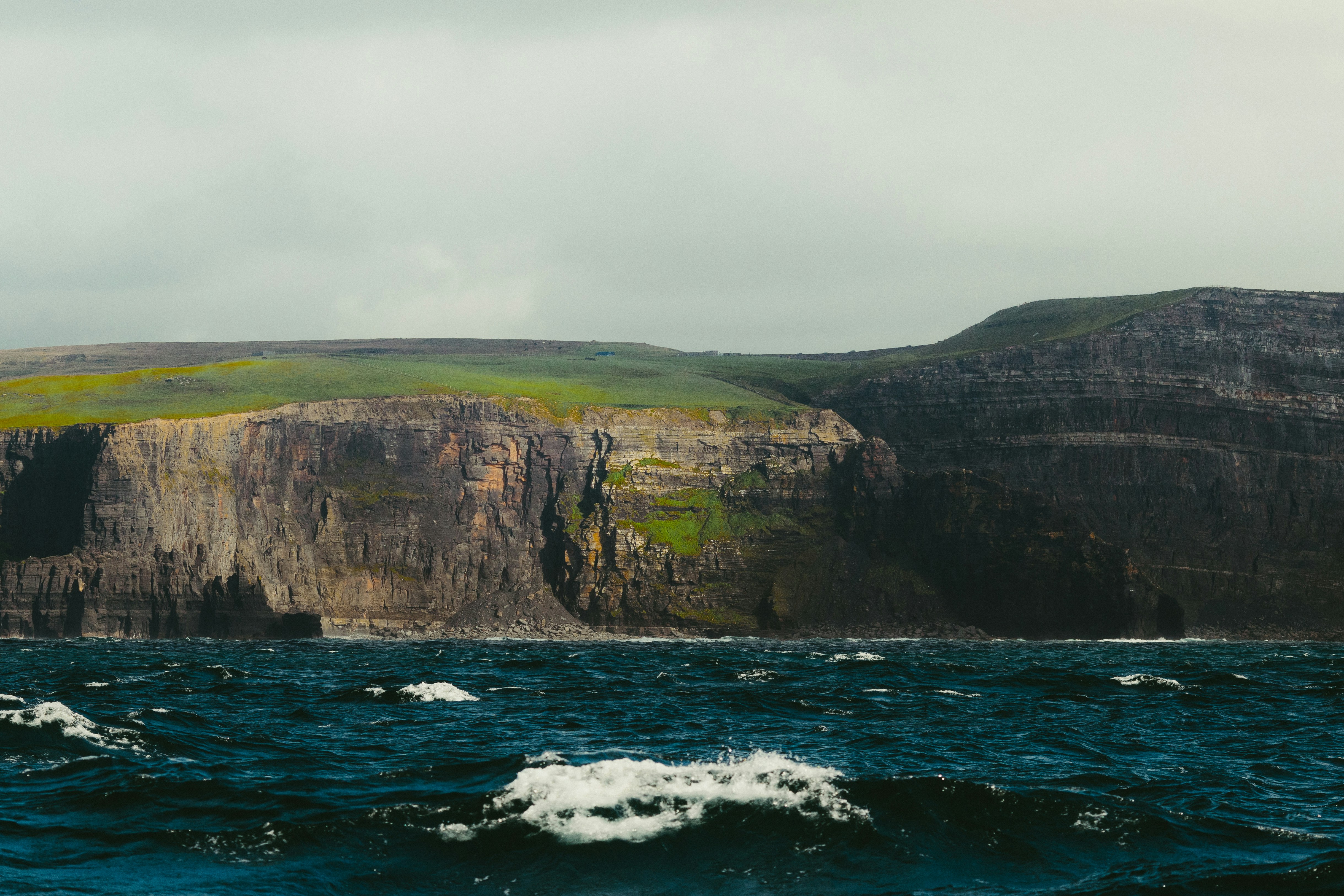 Dramatic cliffs rise above turbulent waters, showcasing a blend of green landscapes and rugged rock formations. The scene captures the essence of nature's power and beauty.