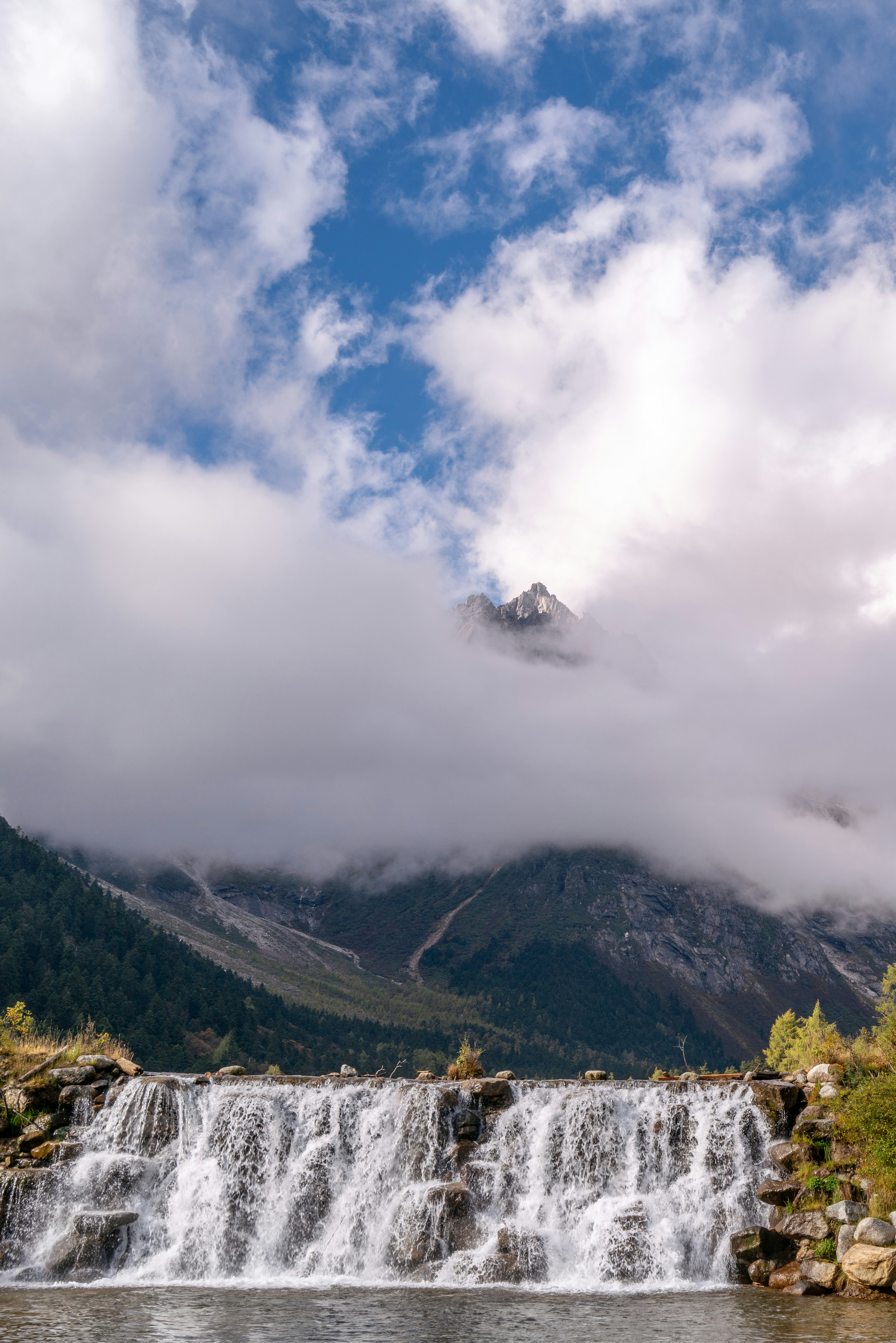 Waterfall cascades down rocky mountainside under clouds photo – Free ...