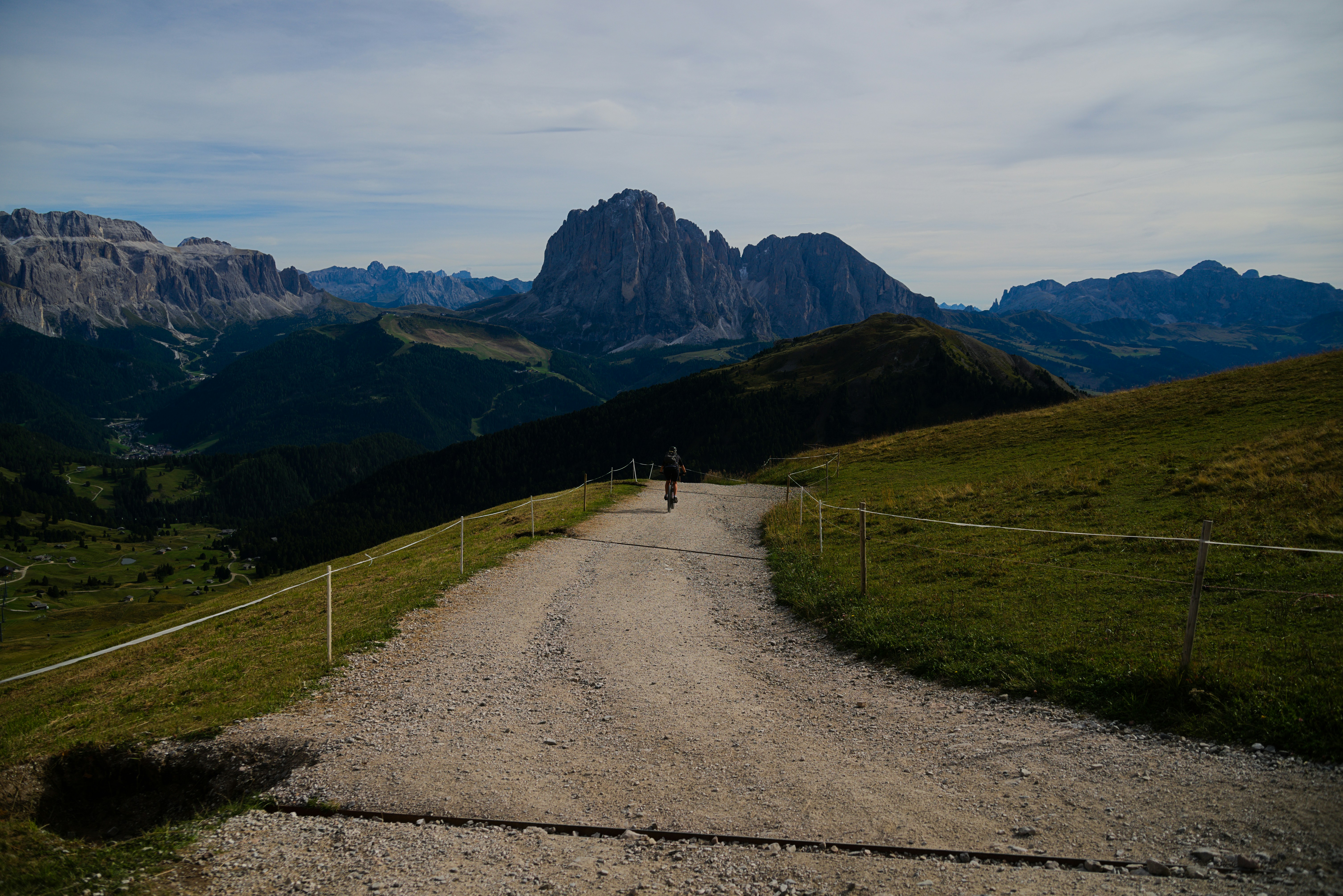 Gravel path leads to majestic mountain peaks under blue sky.