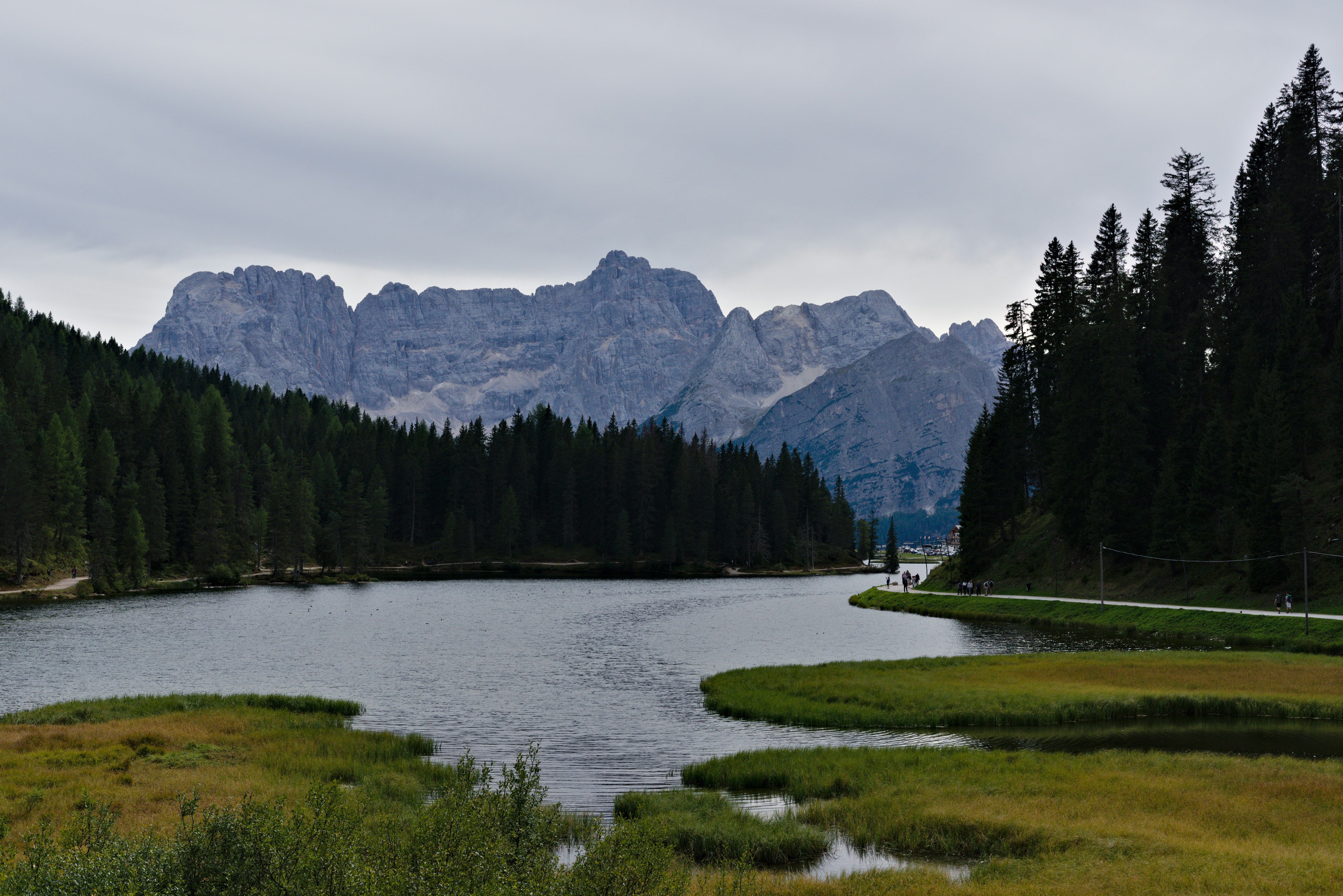 Lake with pine trees and mountains under cloudy sky