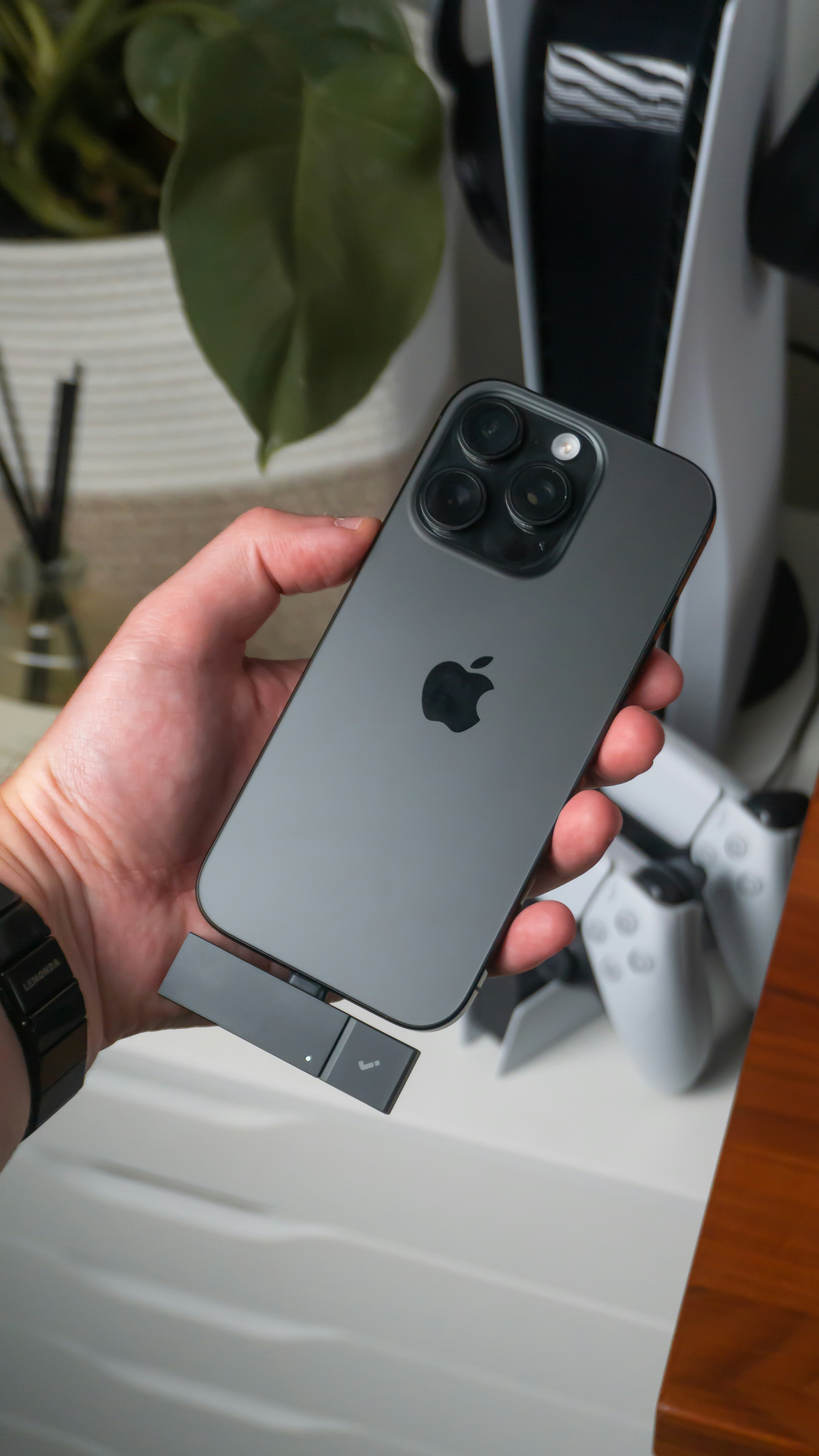 I shot these photos of the HiDock P1 Mini around my home office and living space — a compact AI voice recorder that fits perfectly into any modern desk setup or work-from-home routine. I wanted to capture how portable and functional it is, while keeping that clean, minimalist desk aesthetic I always aim for. Perfect for anyone into tech setups, productivity, or workspace inspiration. – Matúš (@matgocman) | Hand holding dark grey iPhone with accessory attached accessory.