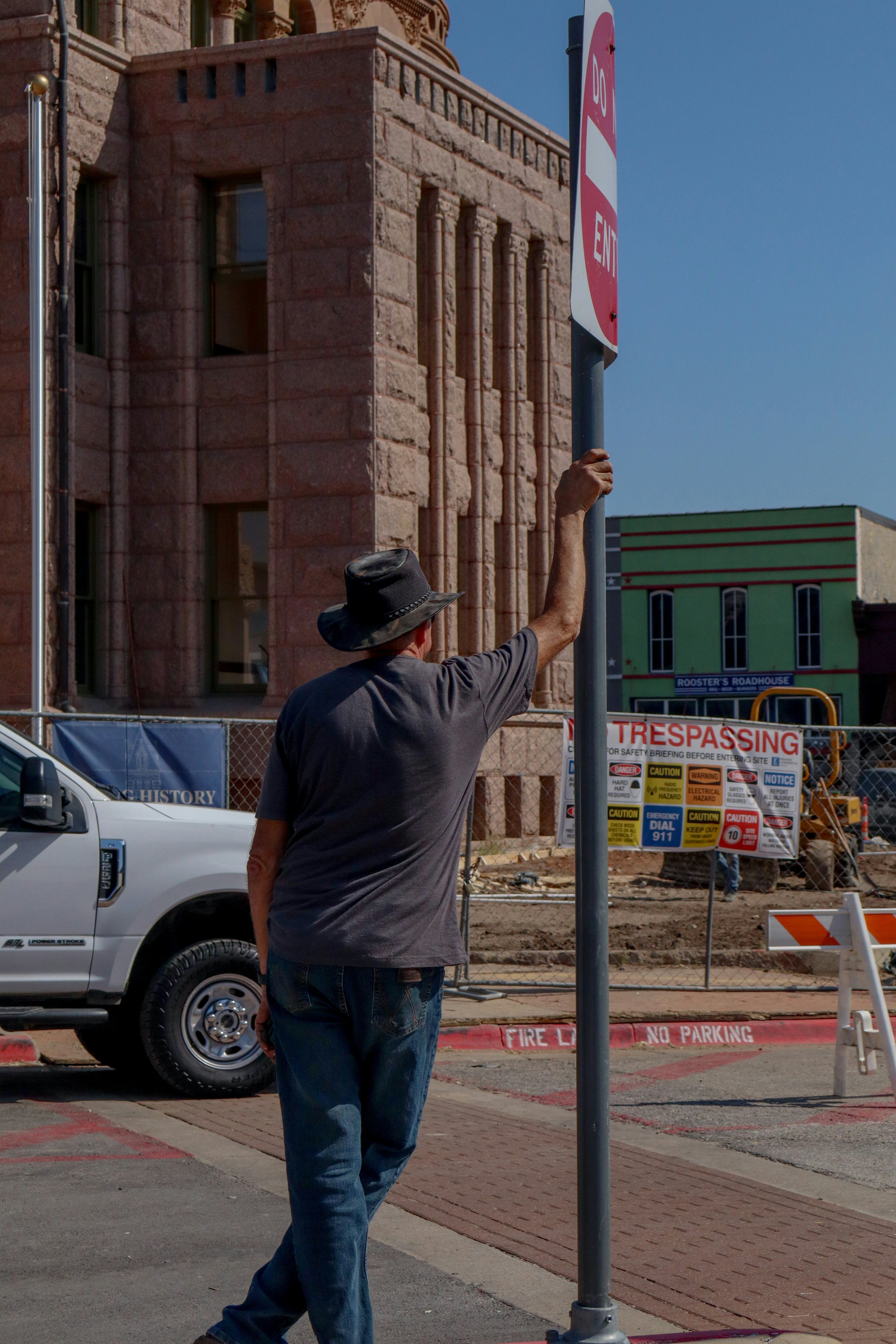 Man in hat leans on pole near construction site.