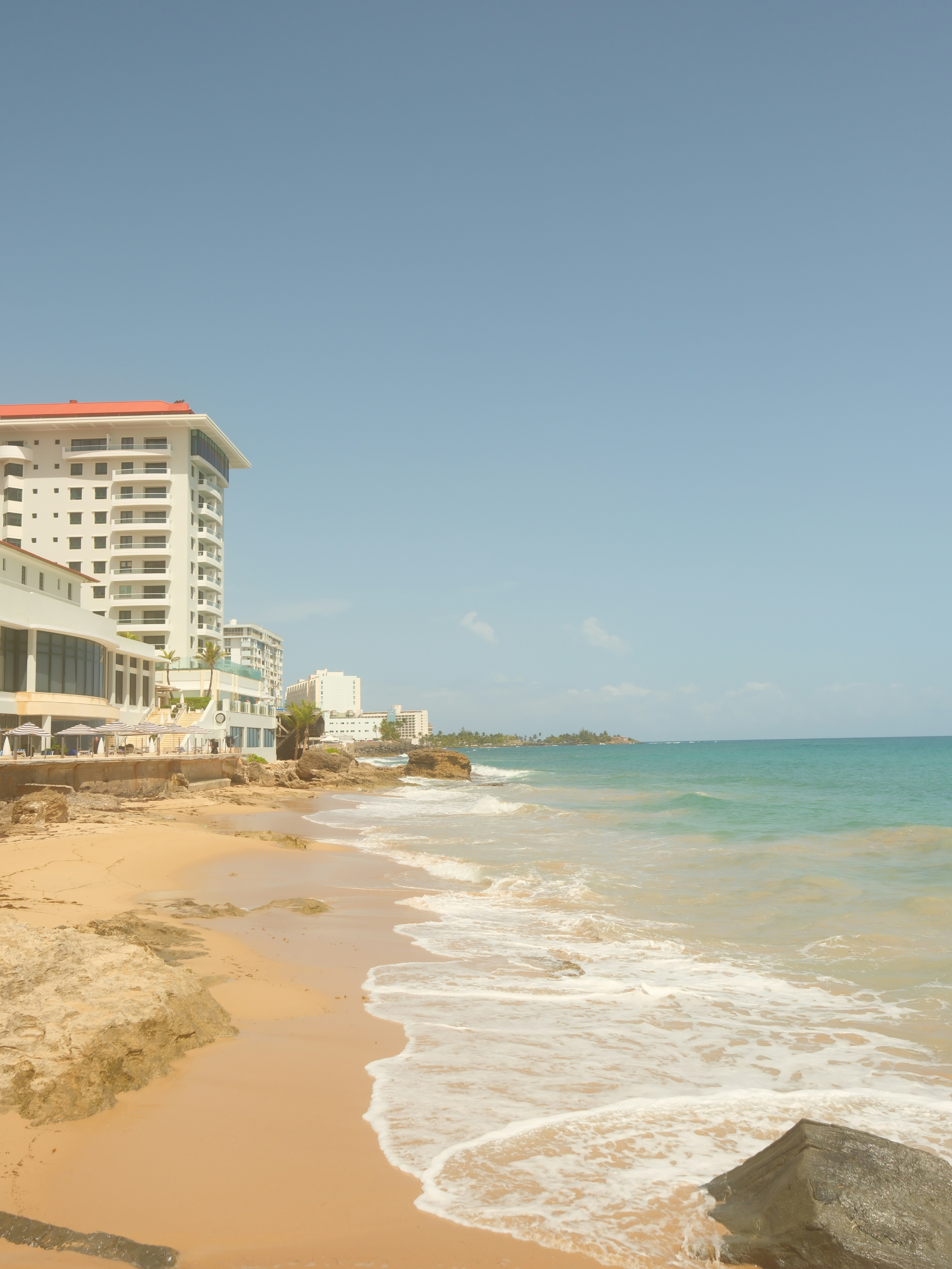 Beach with buildings and ocean waves under blue sky