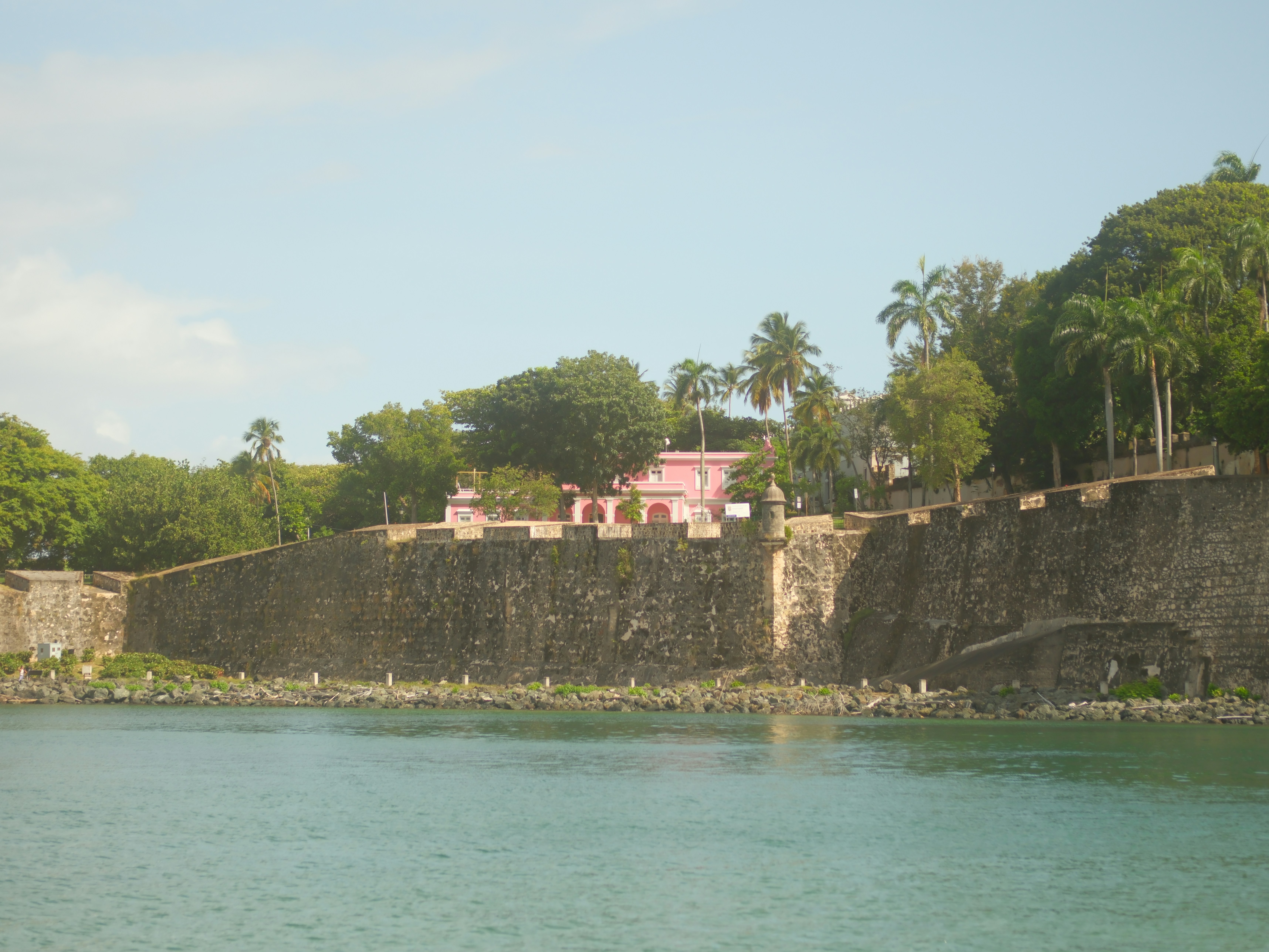 Historic stone fort with pink building and palm trees.