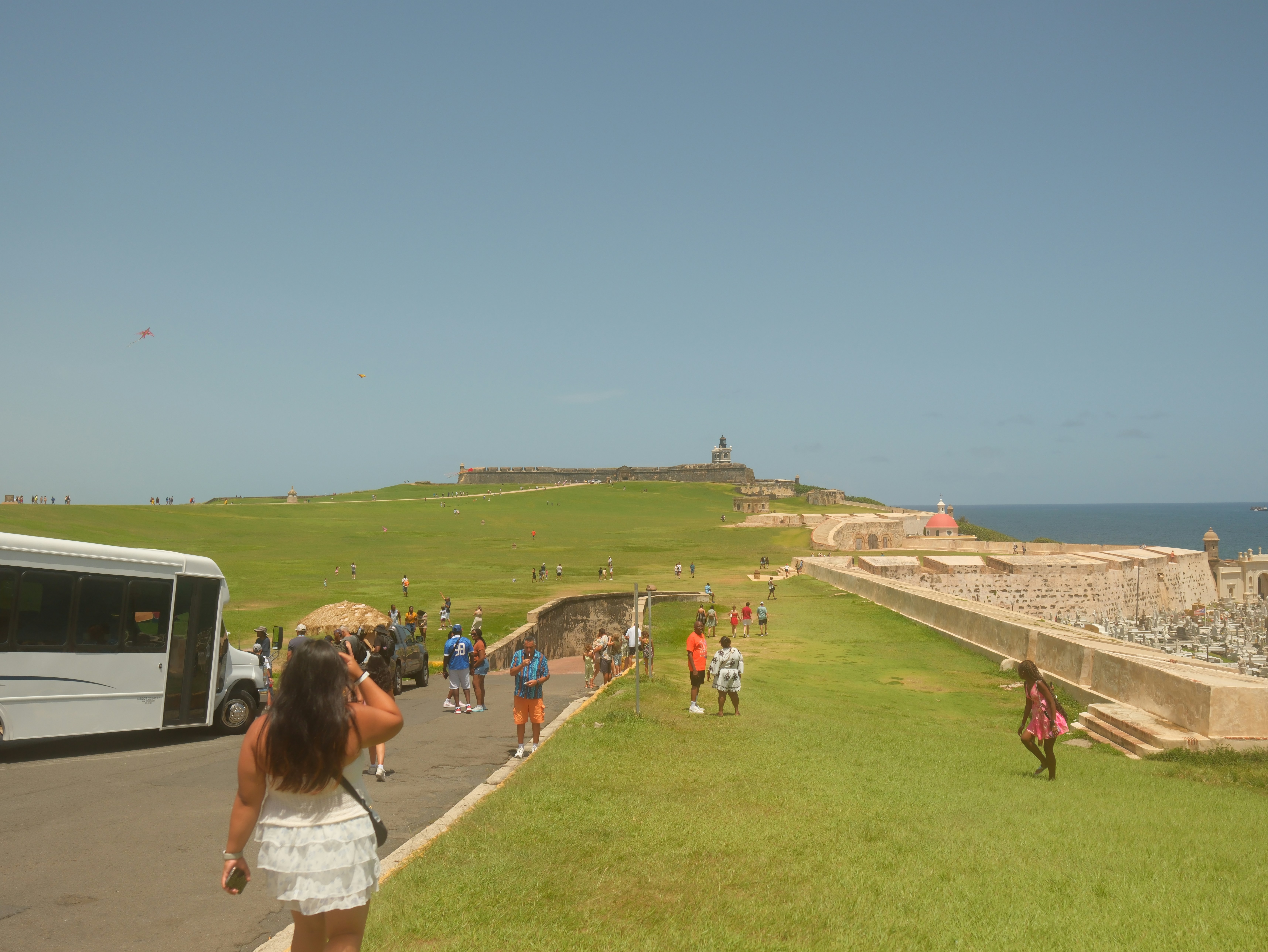 People walking along a grassy path towards a distant fort.