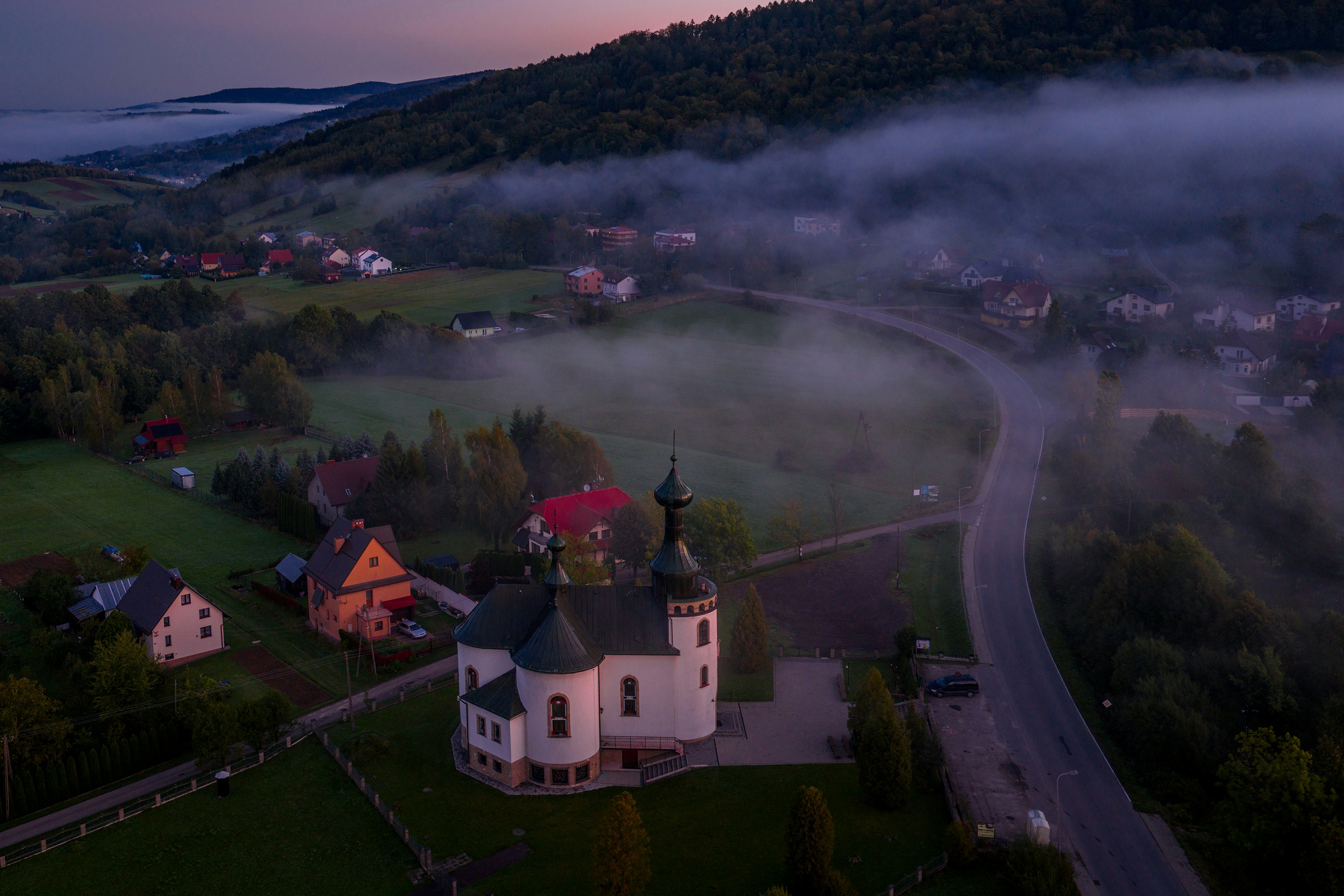Church in Klimkówka, Poland, Beskid Nieski | Church in misty valley at dawn with winding road.