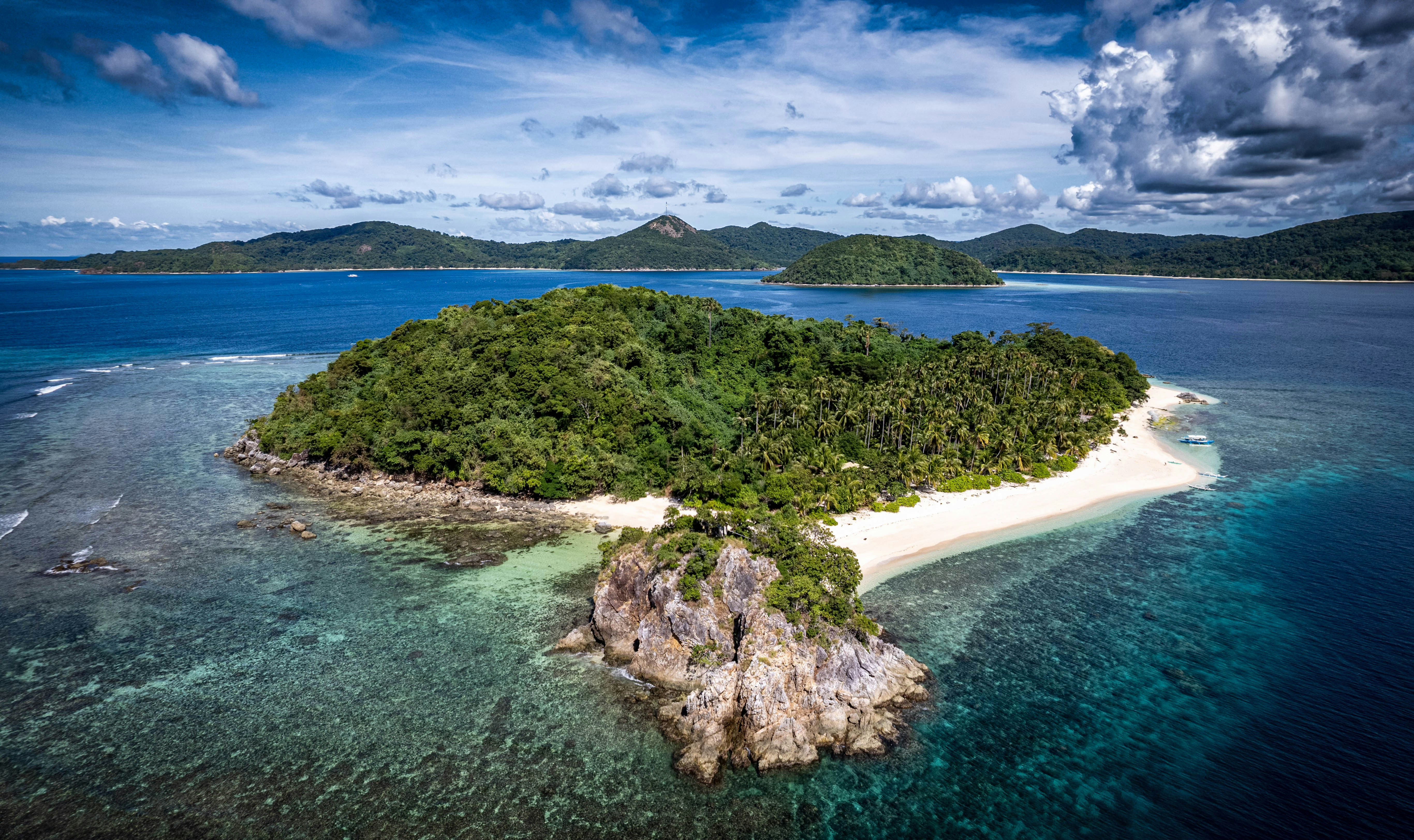 Lush island surrounded by turquoise waters, featuring a sandy beach and rocky outcrops under a vibrant sky.