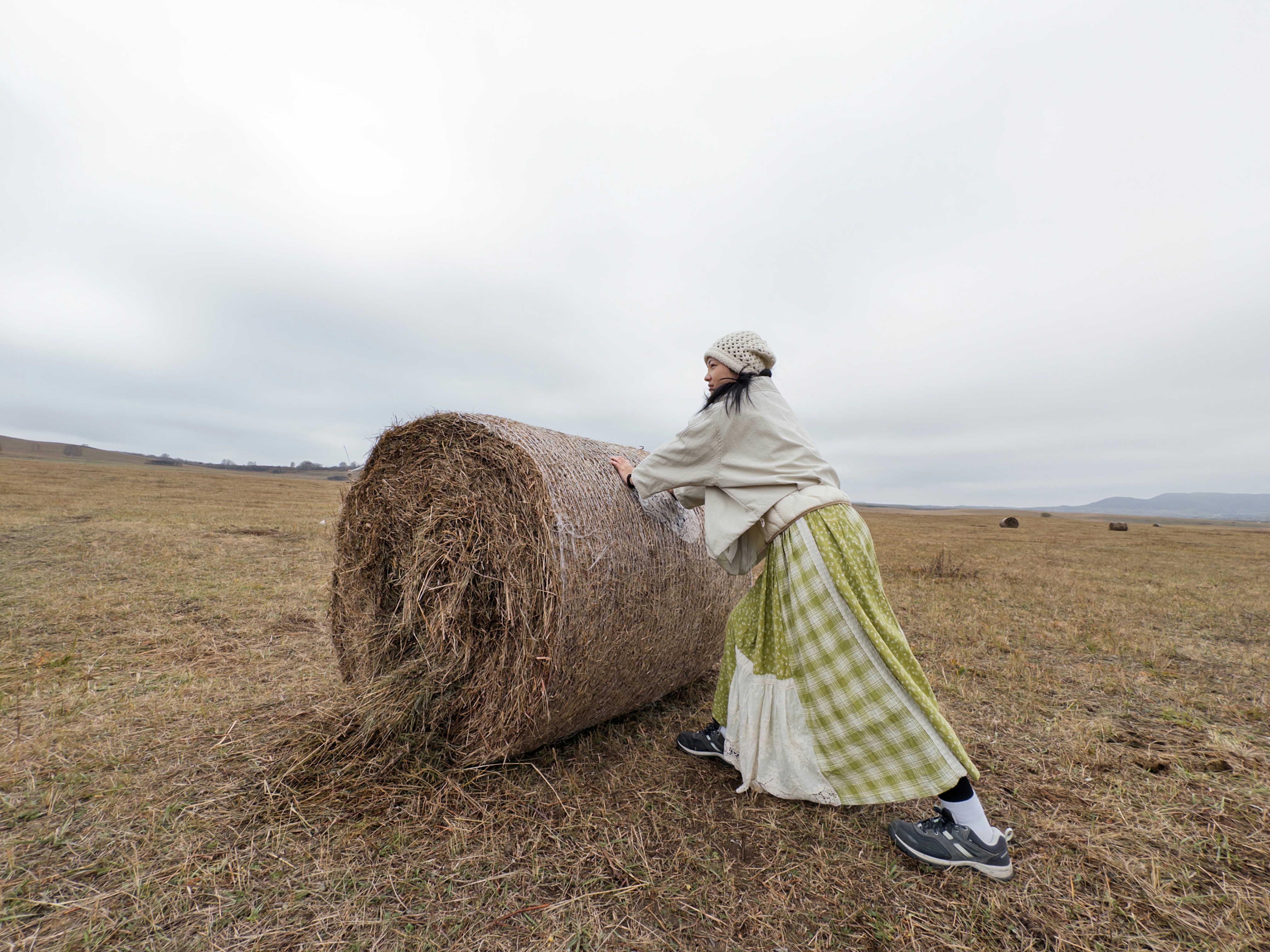 Woman pushing a large hay bale in a field