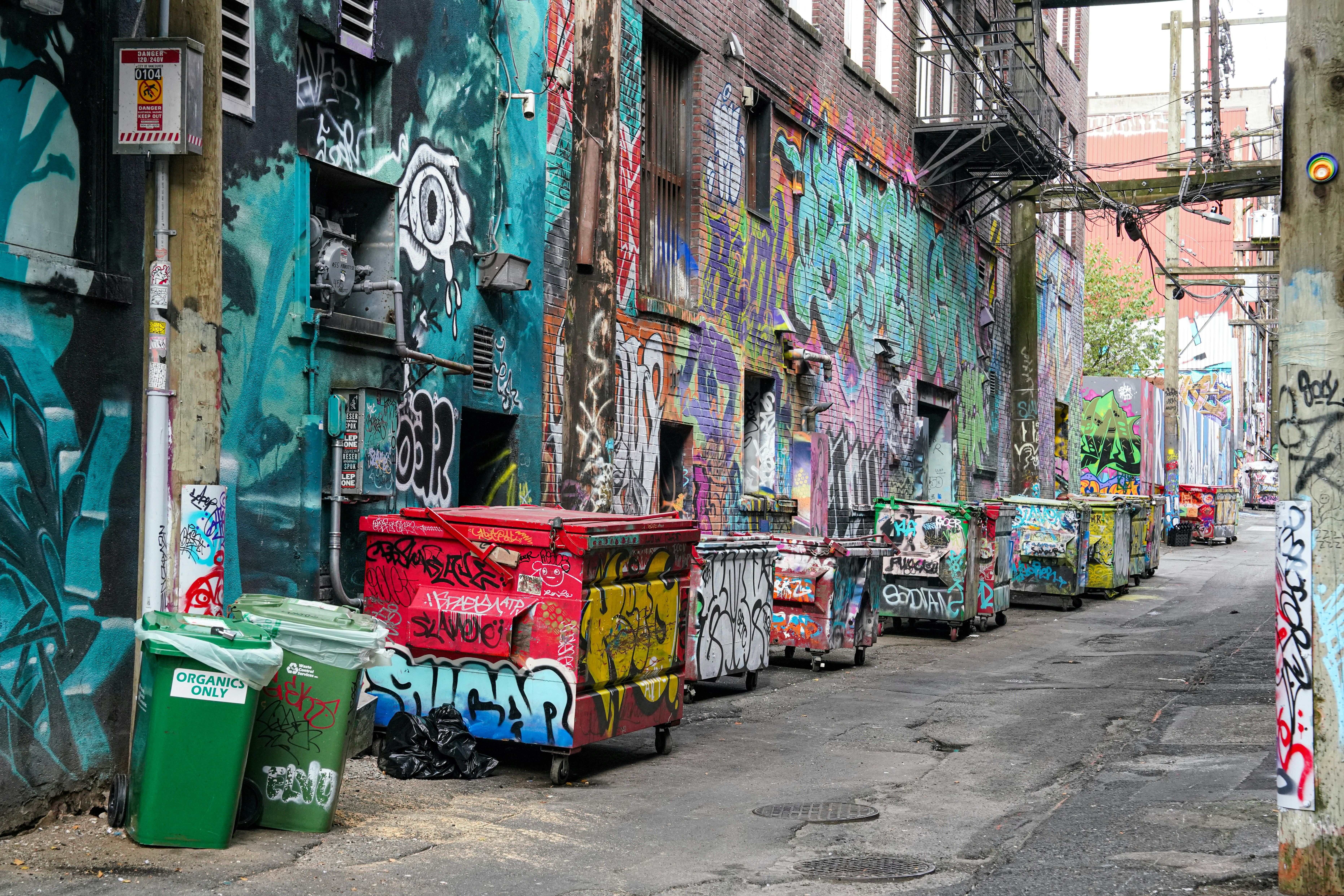 Graffiti-covered alleyway with colorful dumpsters.