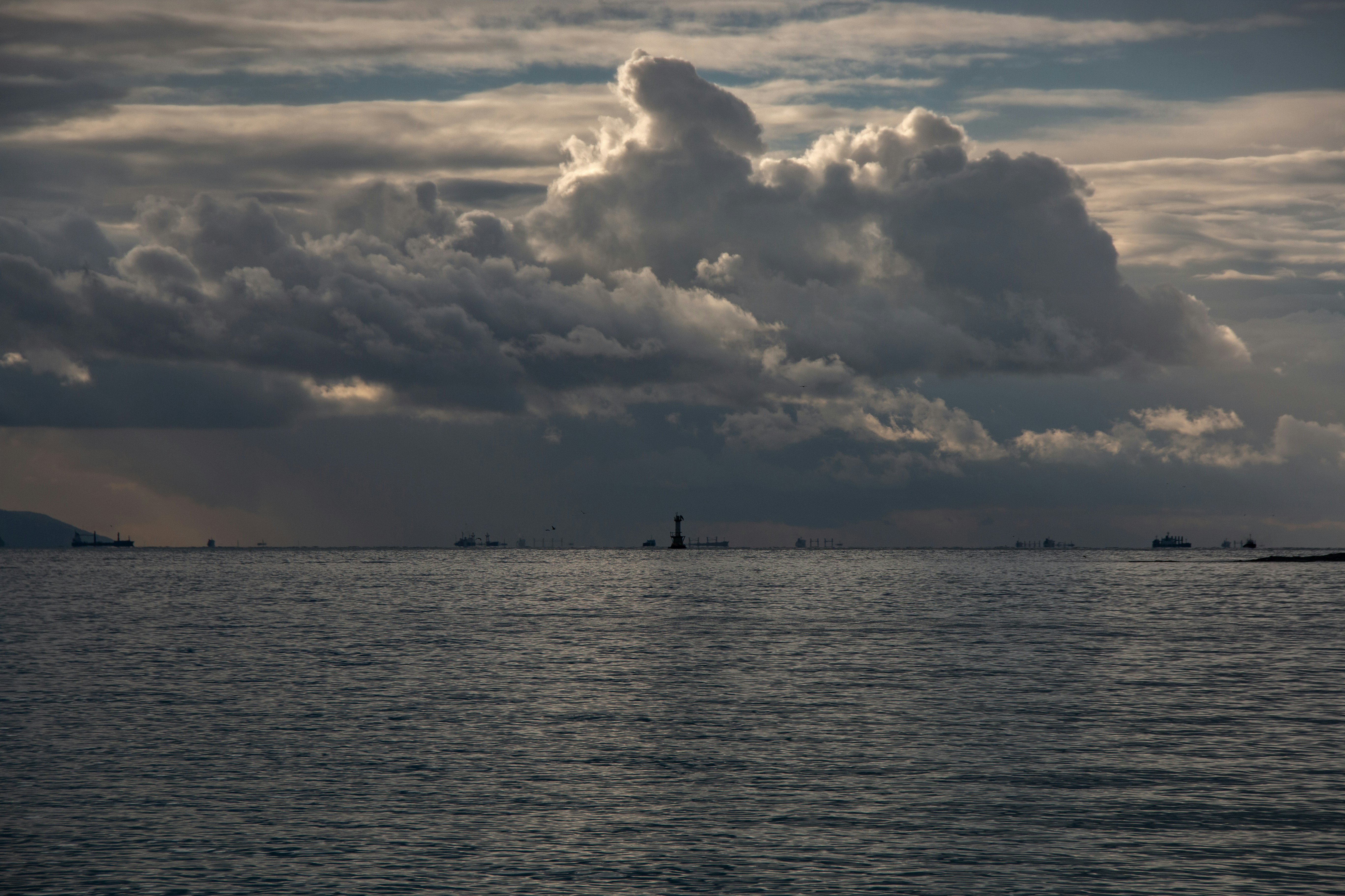 Dramatic clouds over a calm ocean with distant ships.