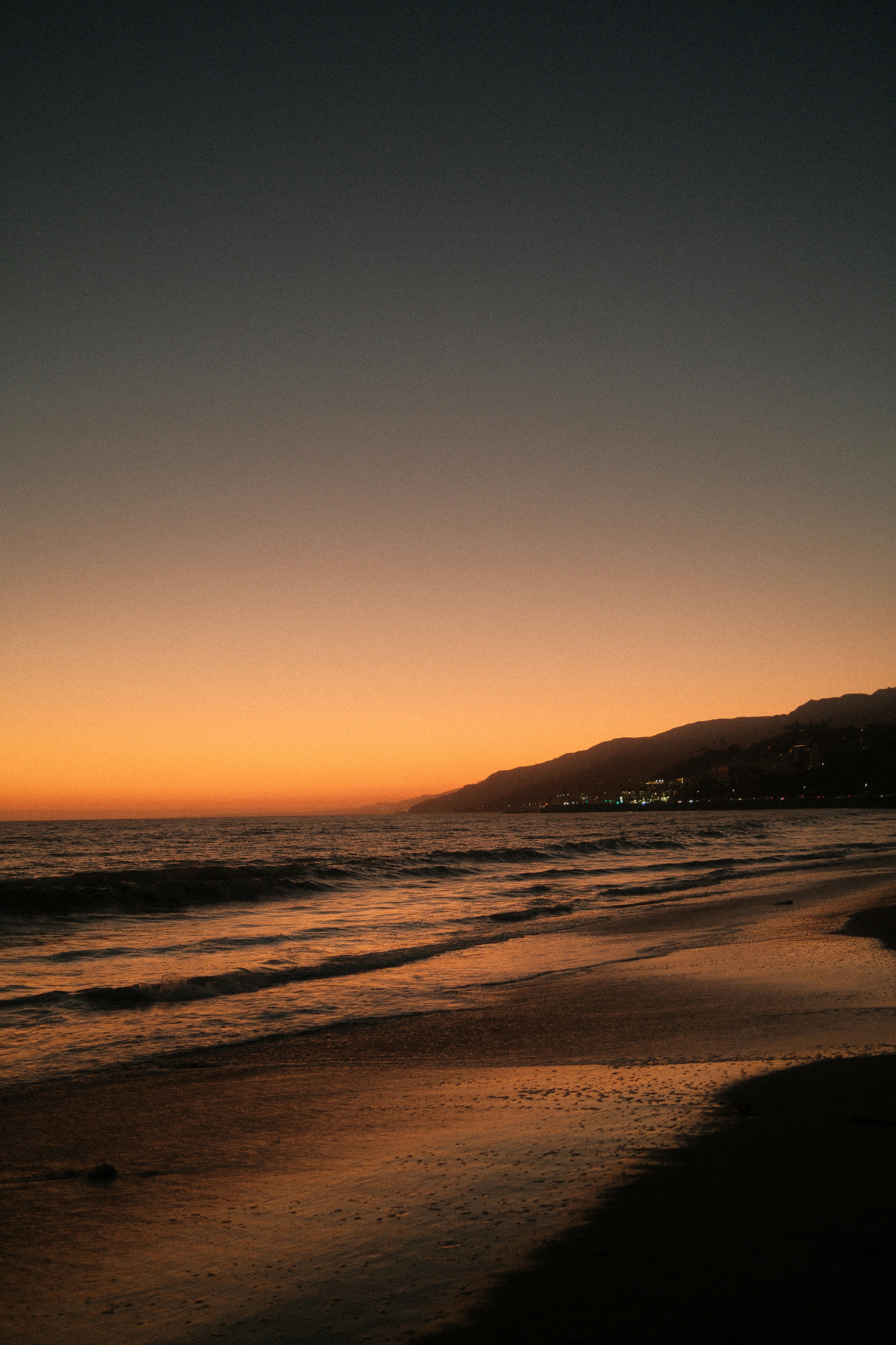 Sunset over a calm ocean with distant lights.