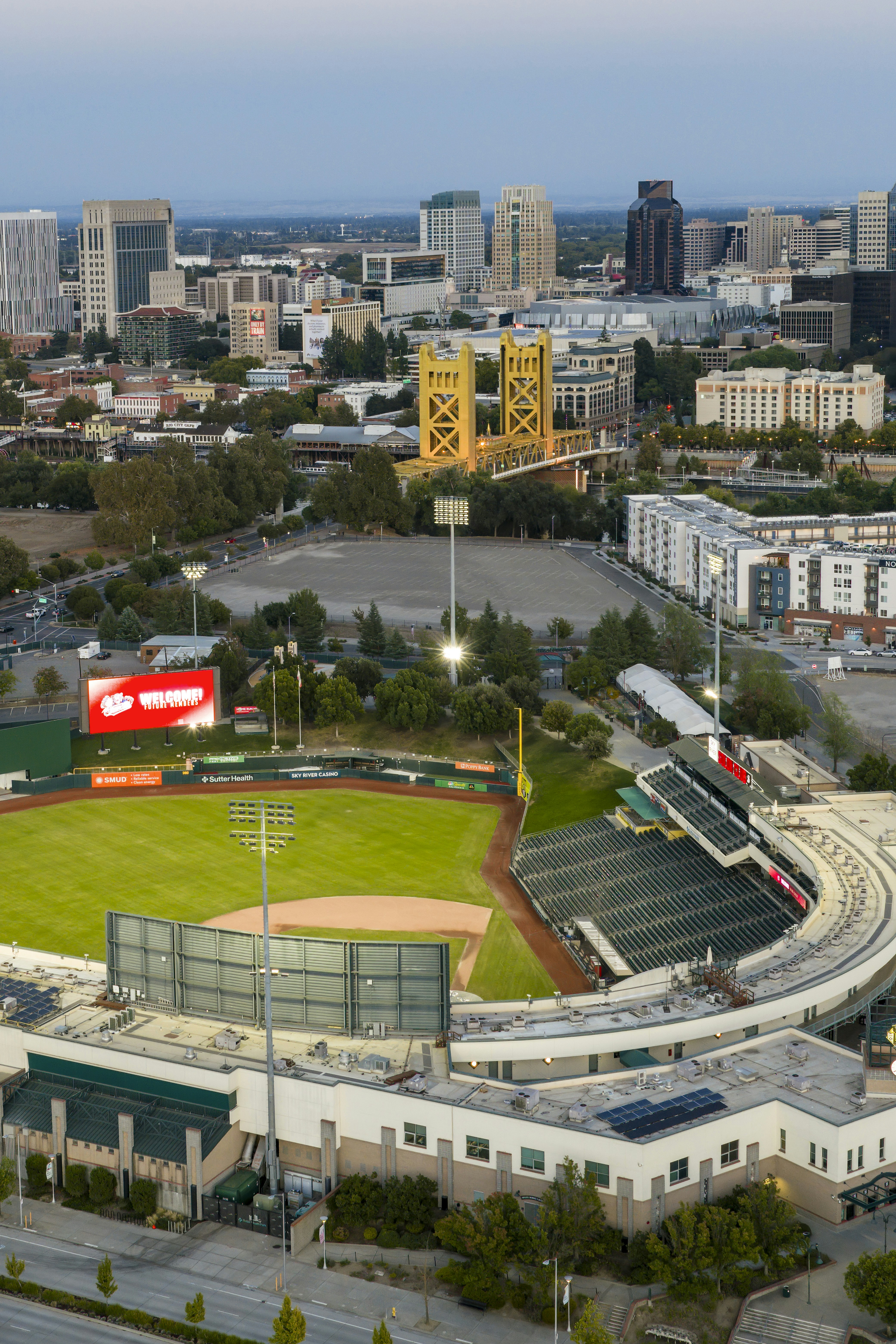 Aerial view showcasing a baseball stadium nestled within Sacramento's urban landscape, with the iconic Golden 1 Center and Tower Bridge in the background.