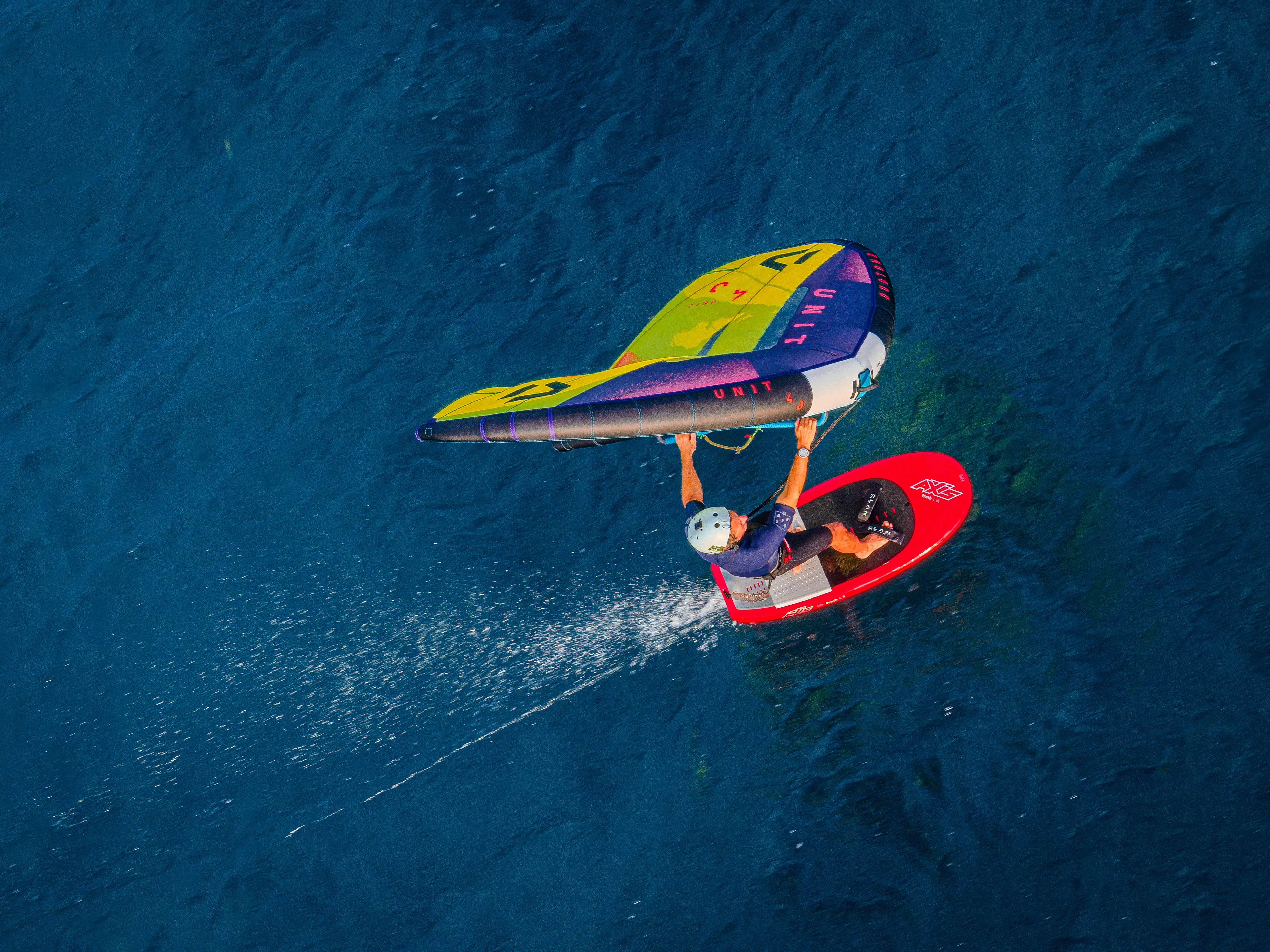 Person wing foiling on a red board over blue water