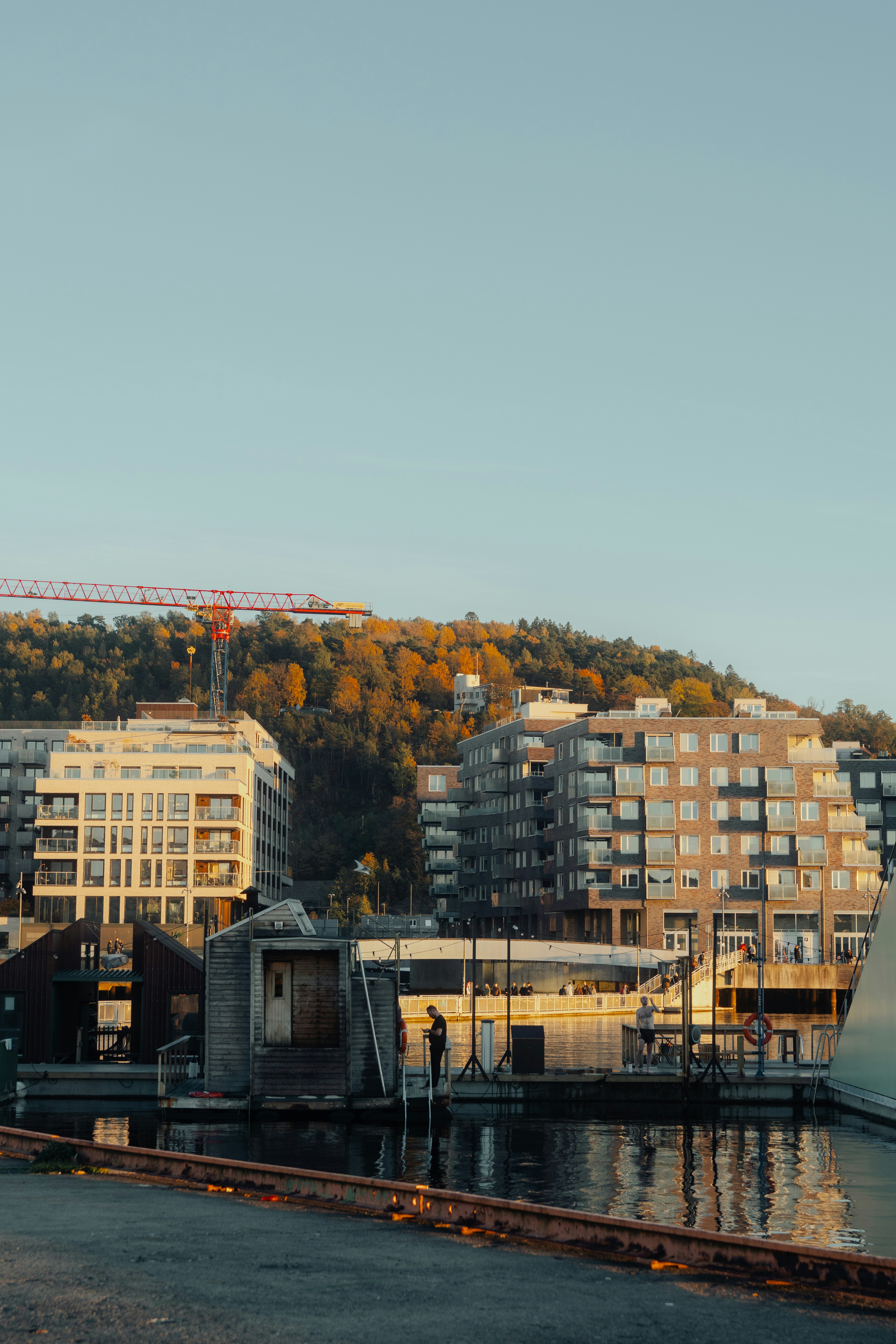Modern buildings overlook a calm harbor at sunset.
