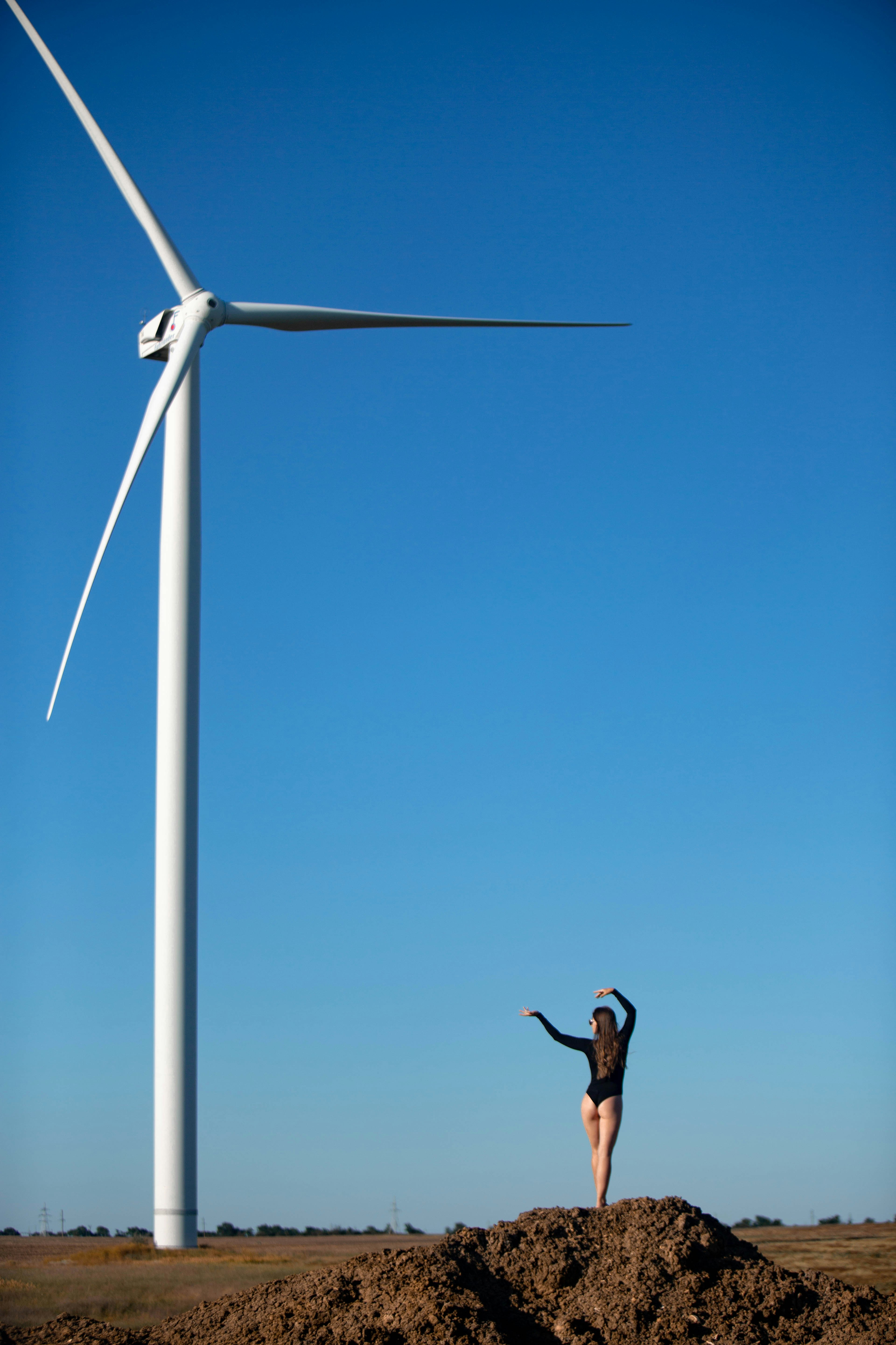 Woman in bodysuit near windmill | Woman dances near a large wind turbine.