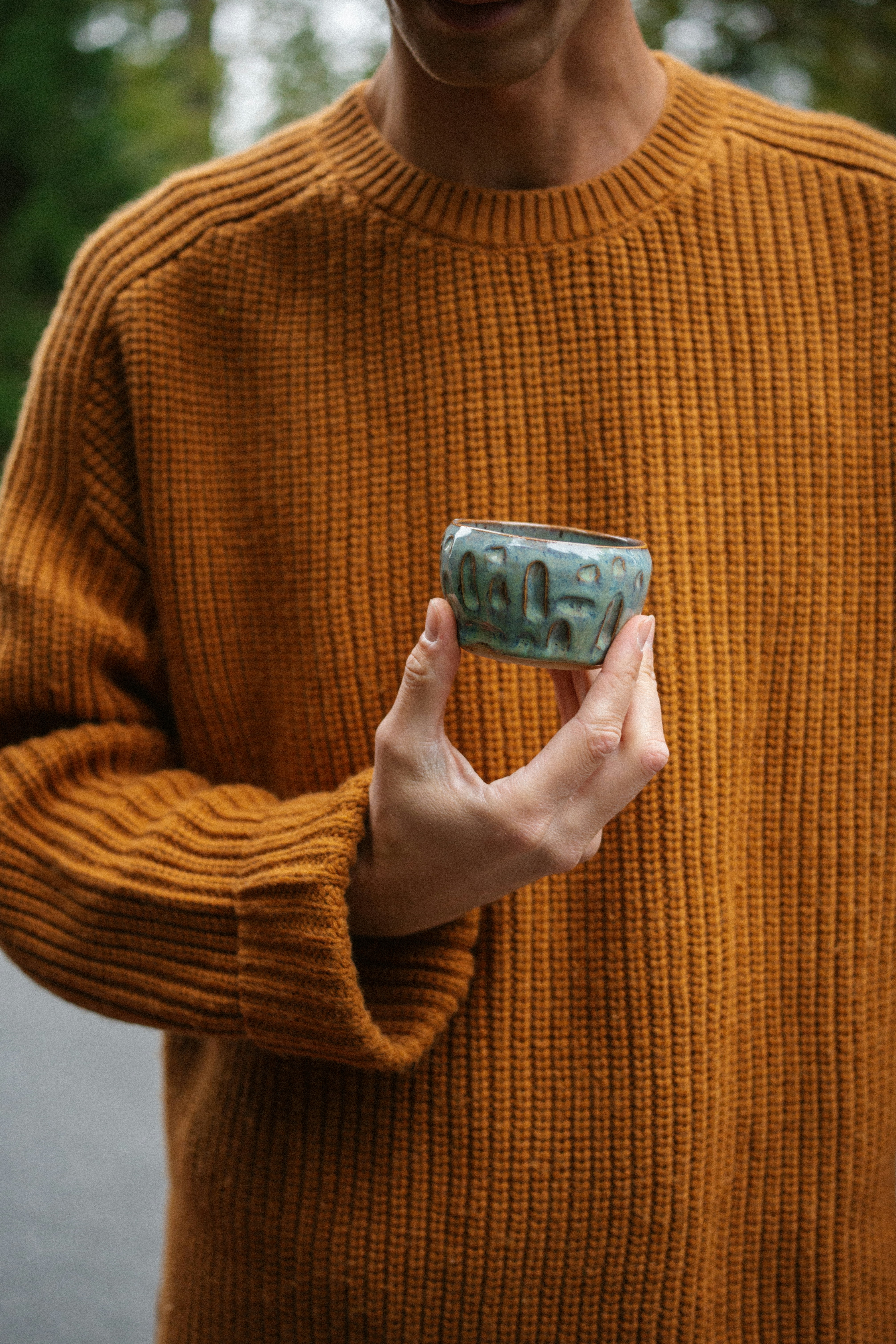 autumn,sweater,ceramics | Man in orange sweater holds small teal ceramic pot.