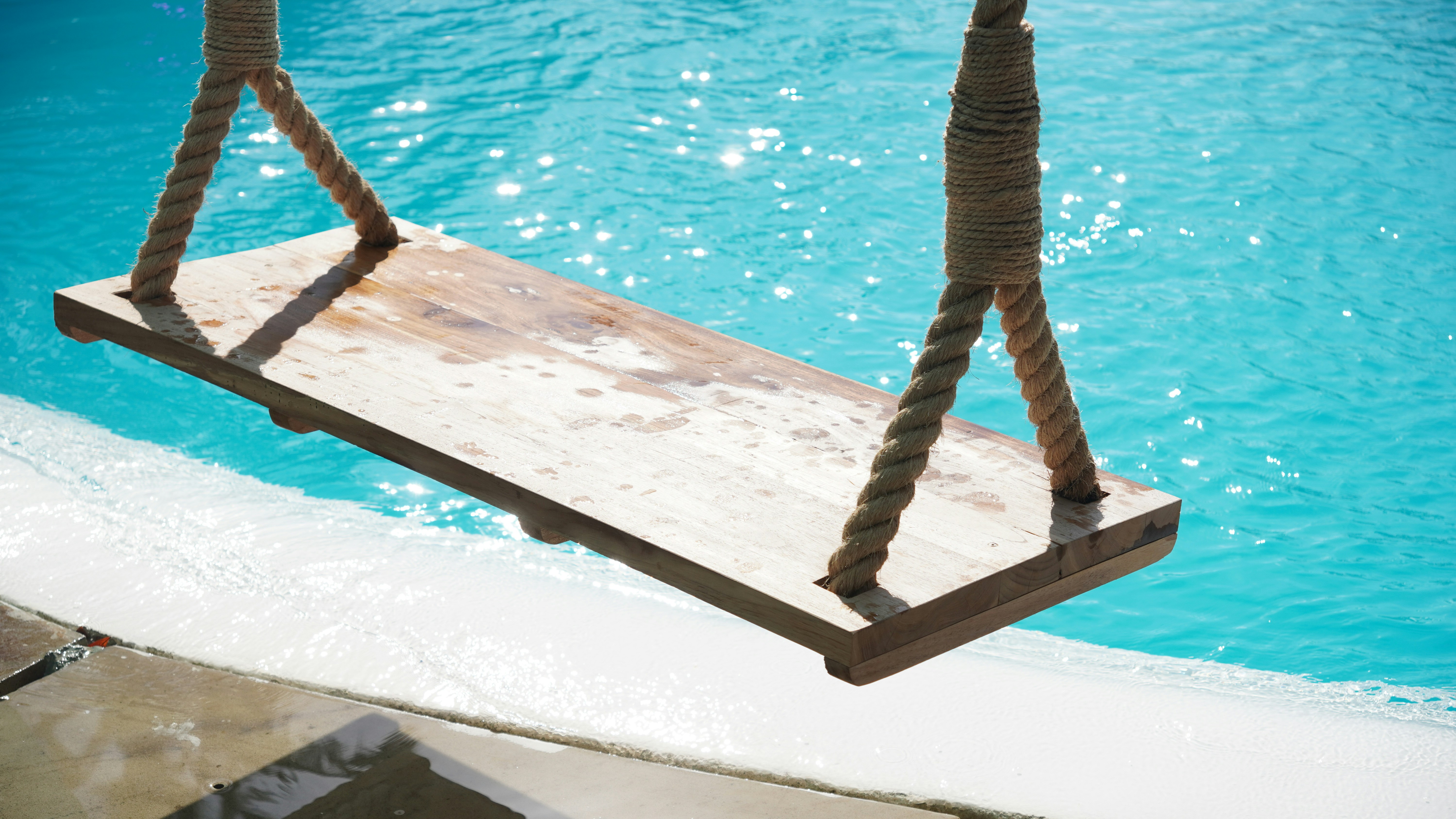 Wooden swing suspended over a sparkling blue pool, inviting relaxation and playfulness.