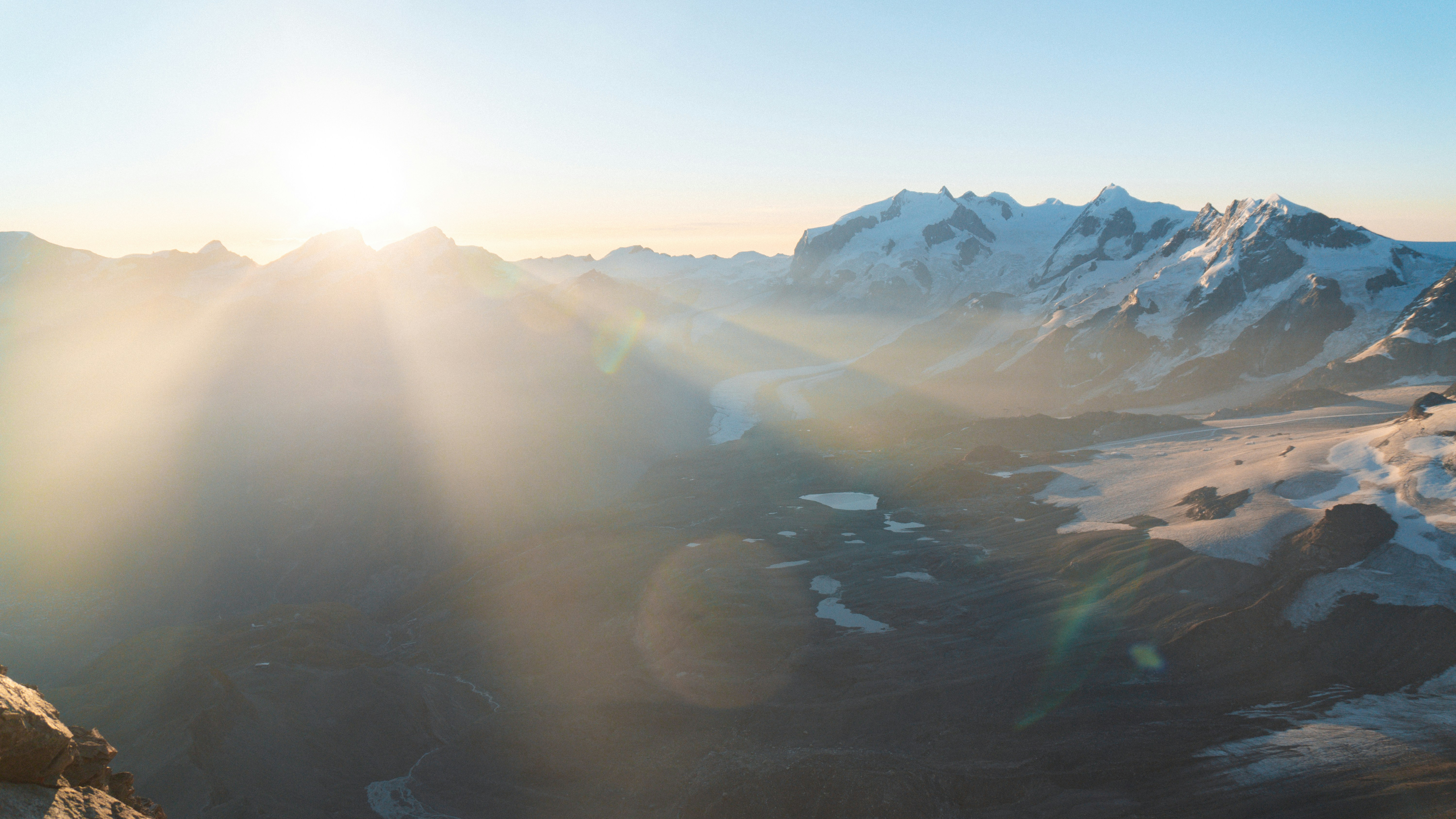 Sunbeams shine over snowy mountain peaks at sunrise.