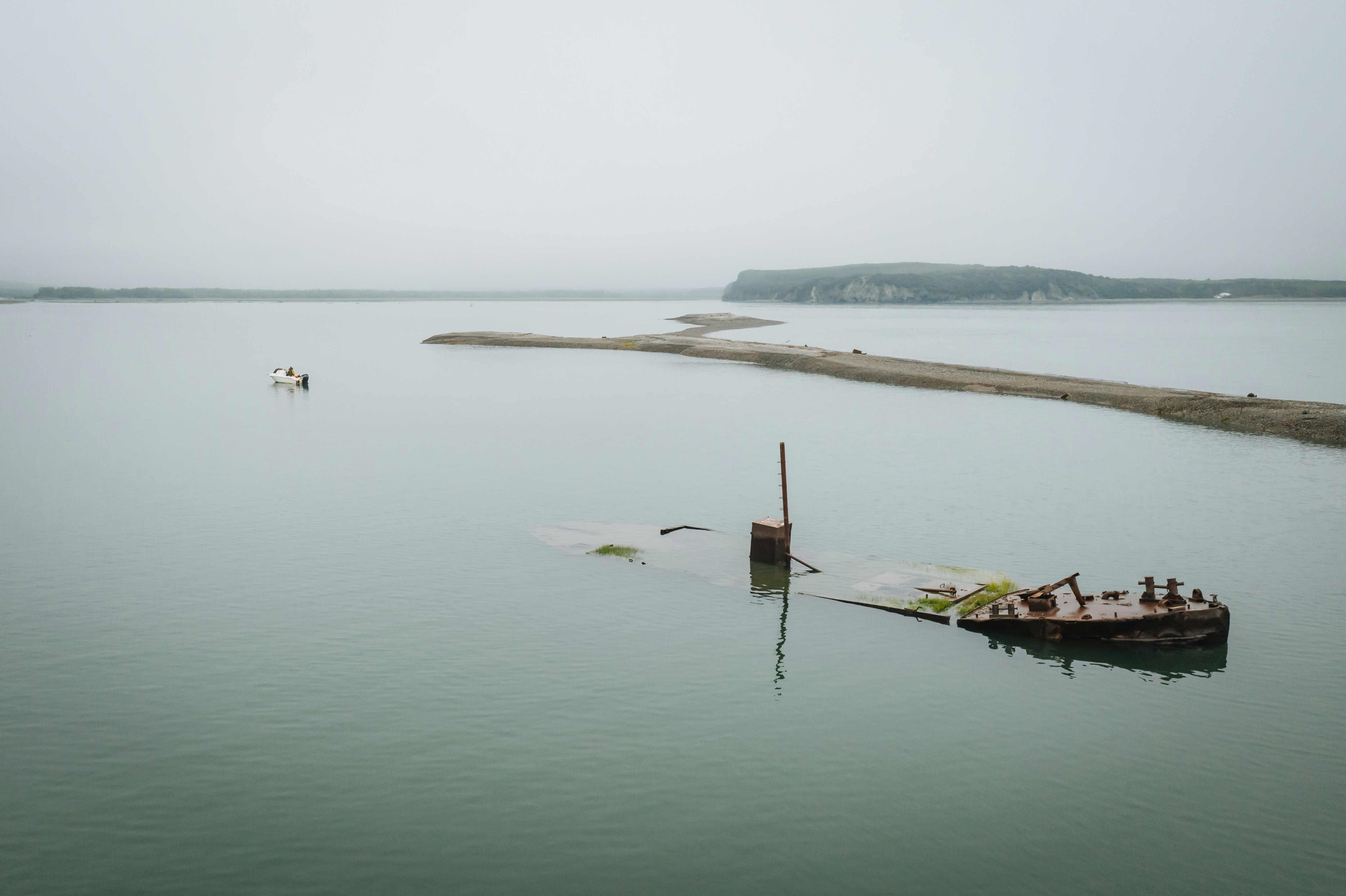 Partially submerged shipwreck in calm, misty water.