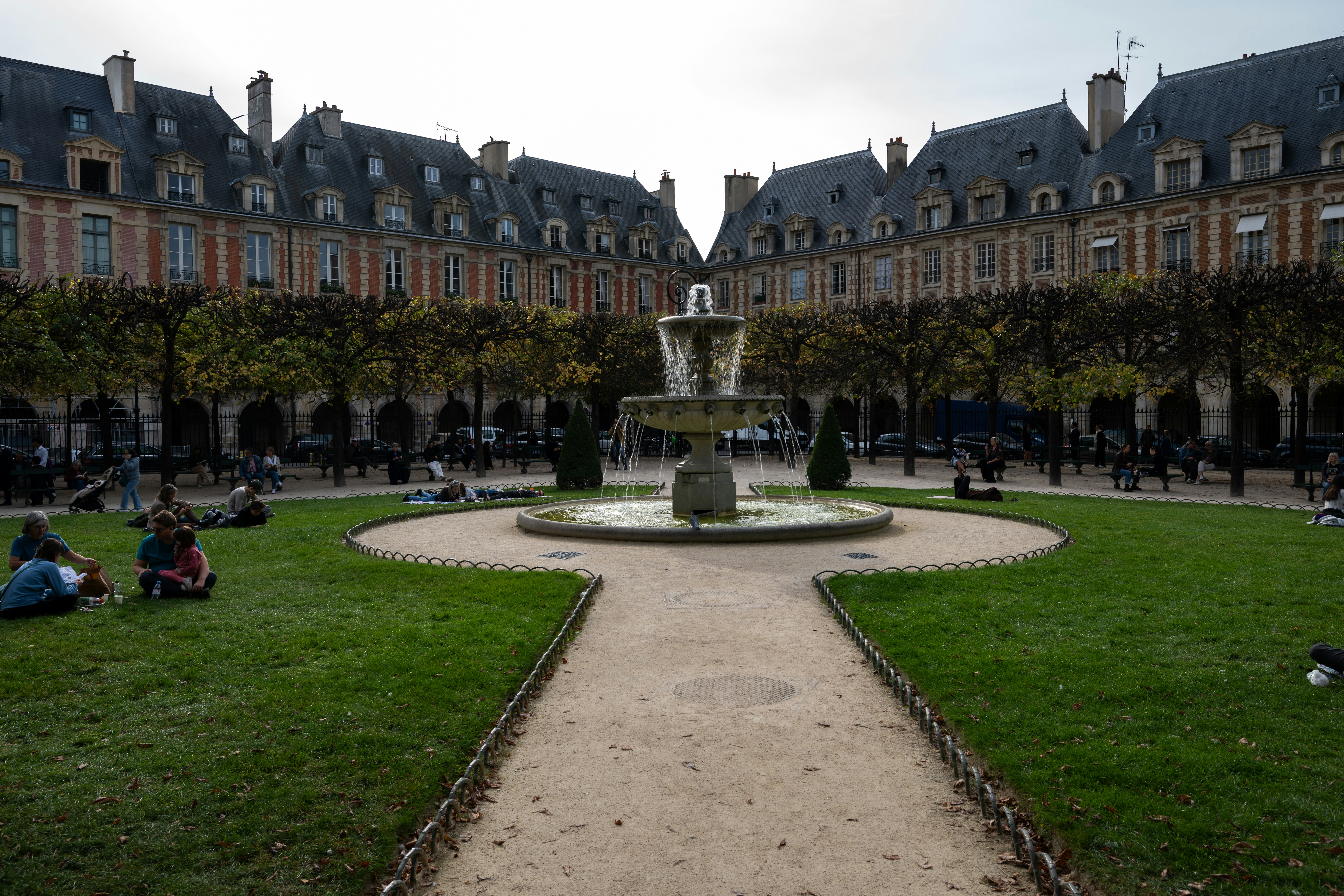People relaxing in a park with a fountain and buildings.