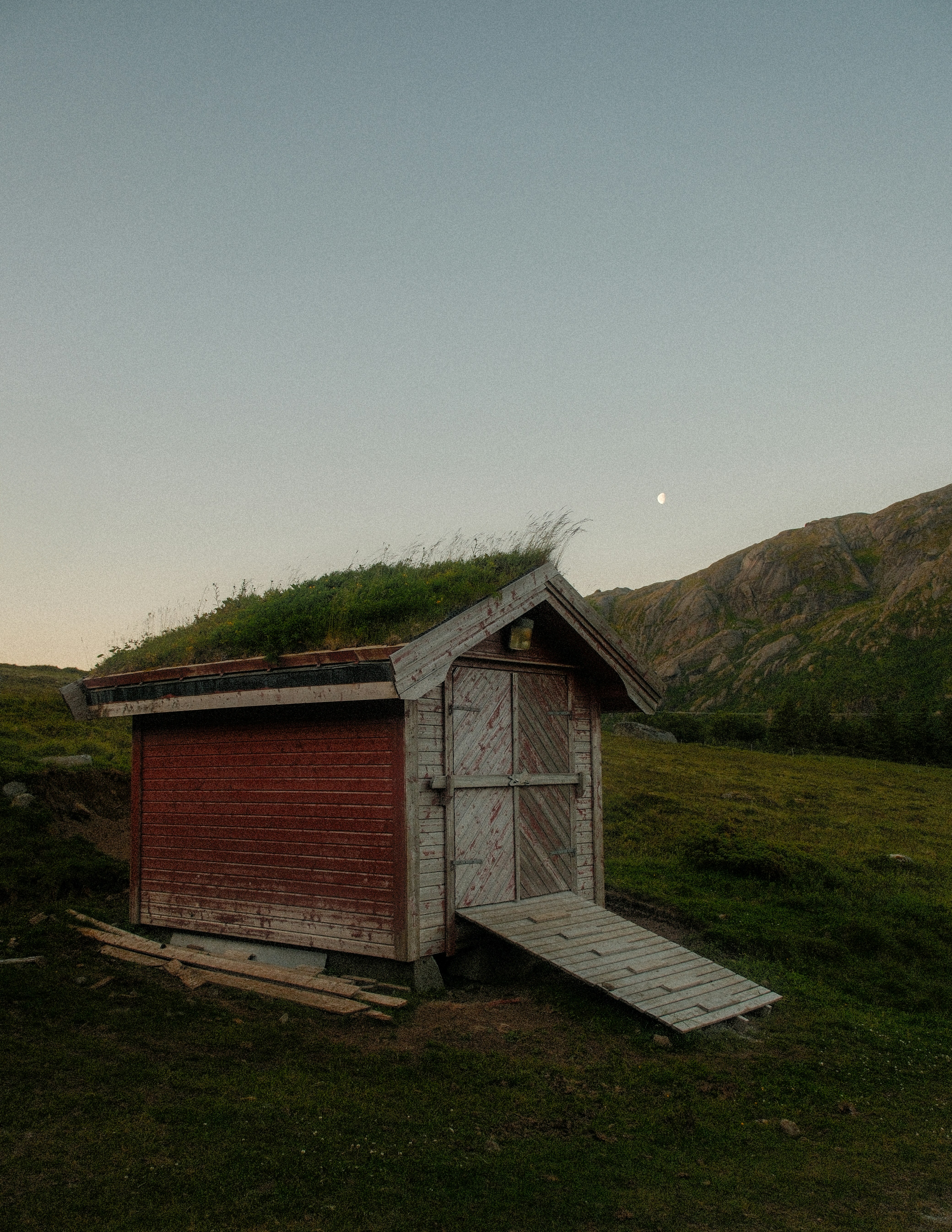 Small red shed with grass roof in grassy landscape