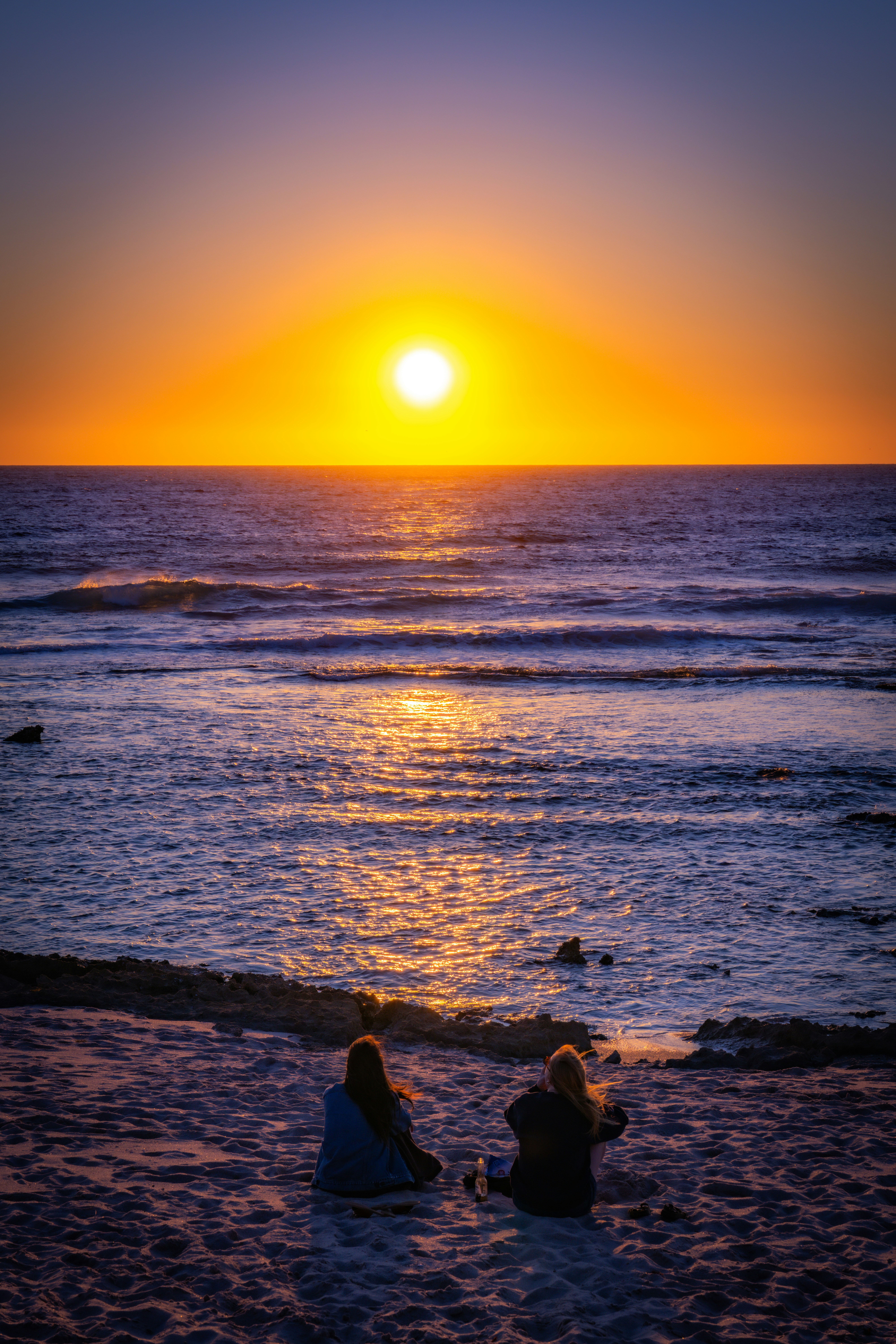 Two people watch the sunset over the ocean.