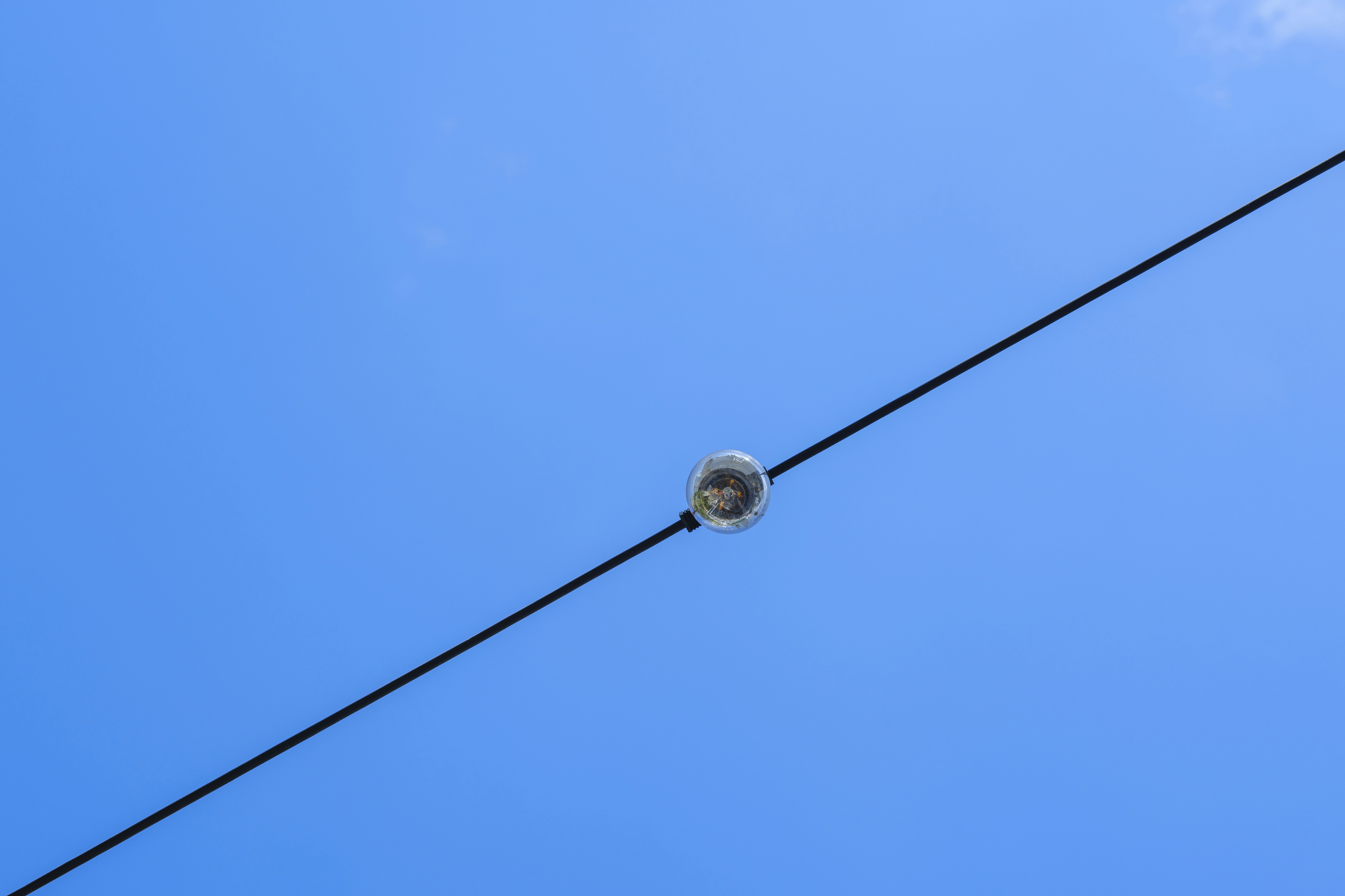 single bulb suspended against clear blue sky | A single light bulb hangs from a wire