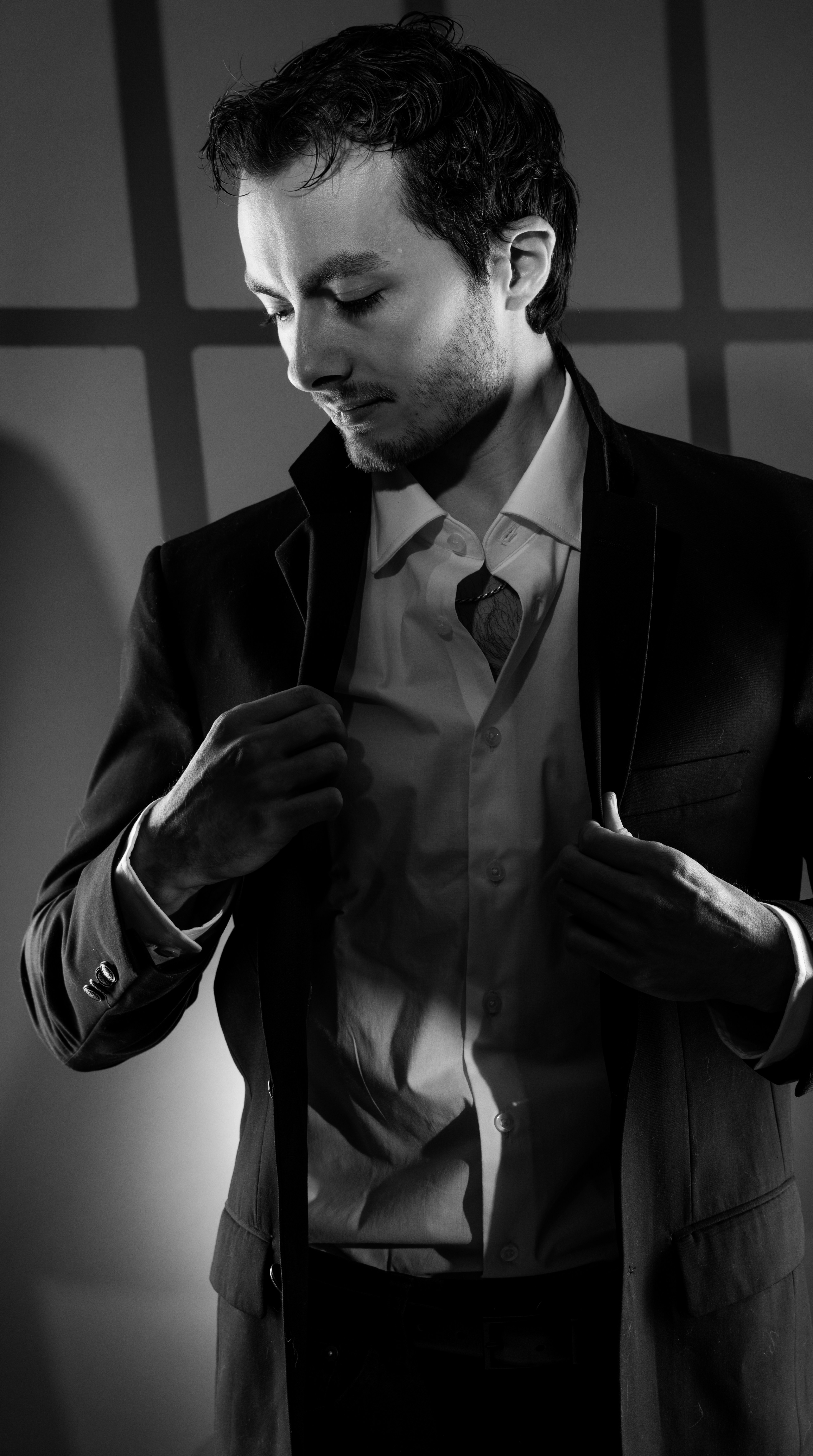 A man adjusting his jacket in a dramatic black and white setting, highlighting the interplay of light and shadow.