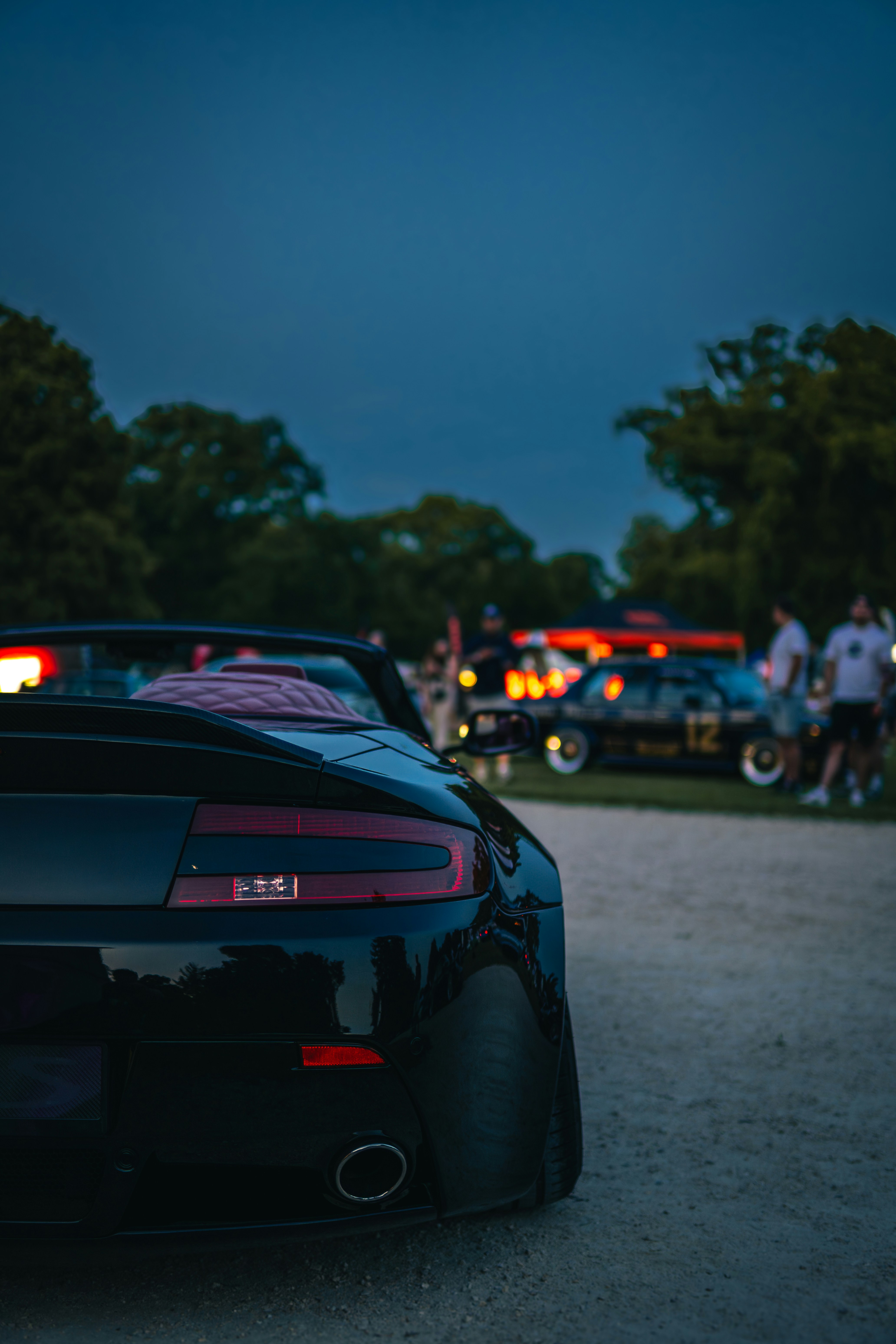 Midnight Contours: Rear Quarter View of a Glossy Sports Car at a Twilight Car Show